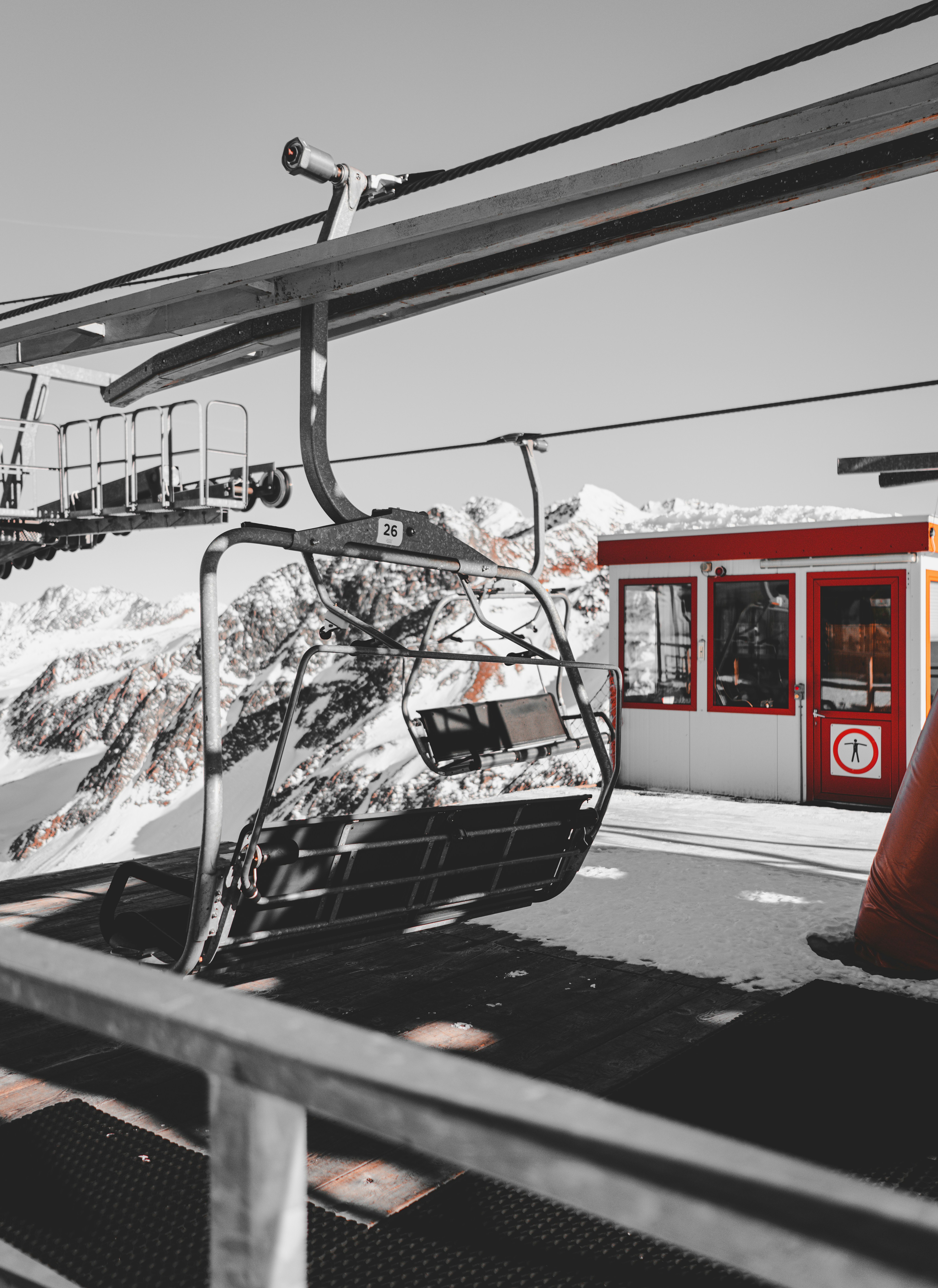 Empty ski chairlift suspended above a snowy landscape with a vibrant red lift station in the background.