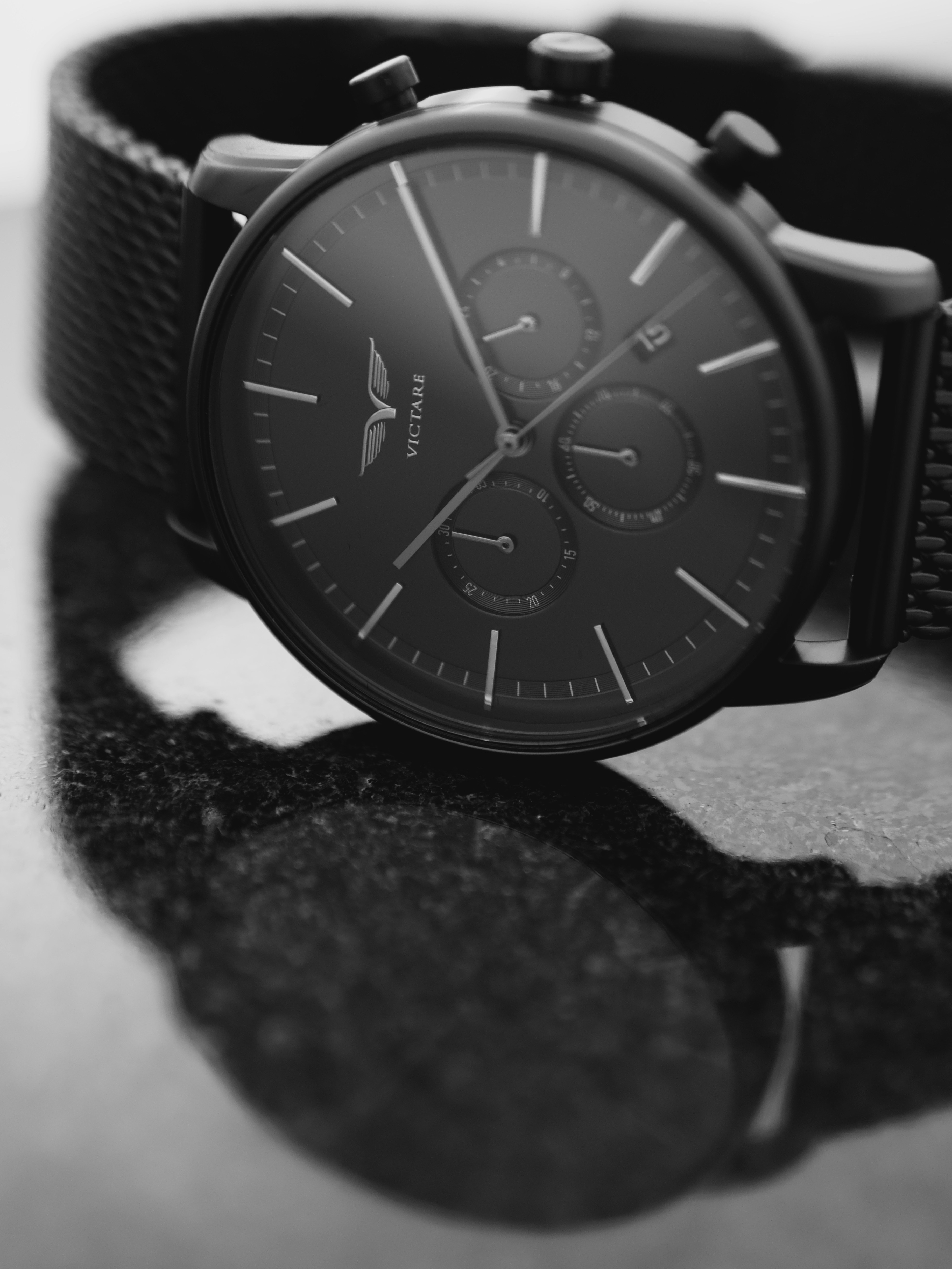 A sleek black chronograph watch resting on a polished surface, showcasing its minimalist design and intricate dial details.