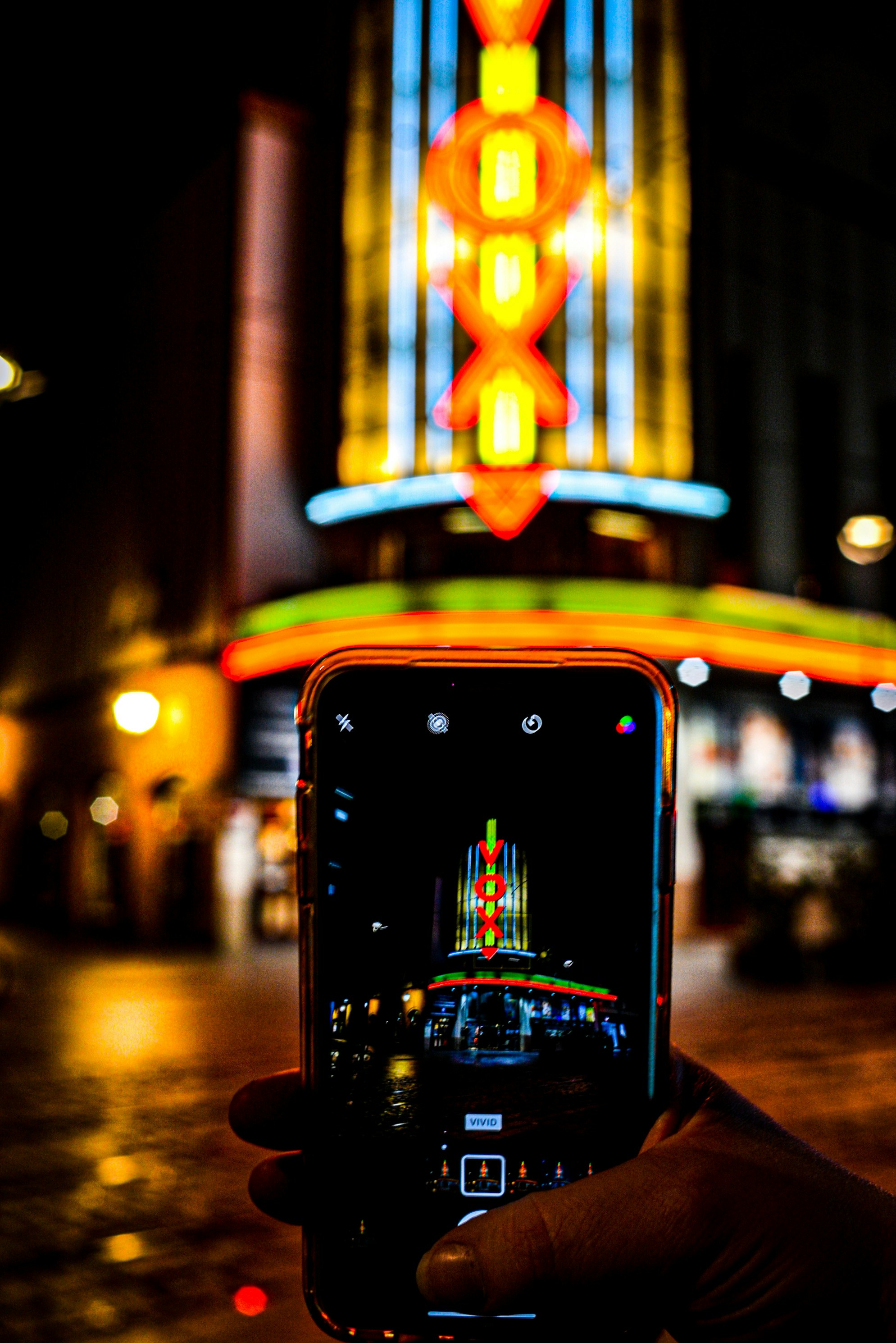 A smartphone captures the vibrant neon lights of a historic theater, showcasing a blend of modern and classic aesthetics.