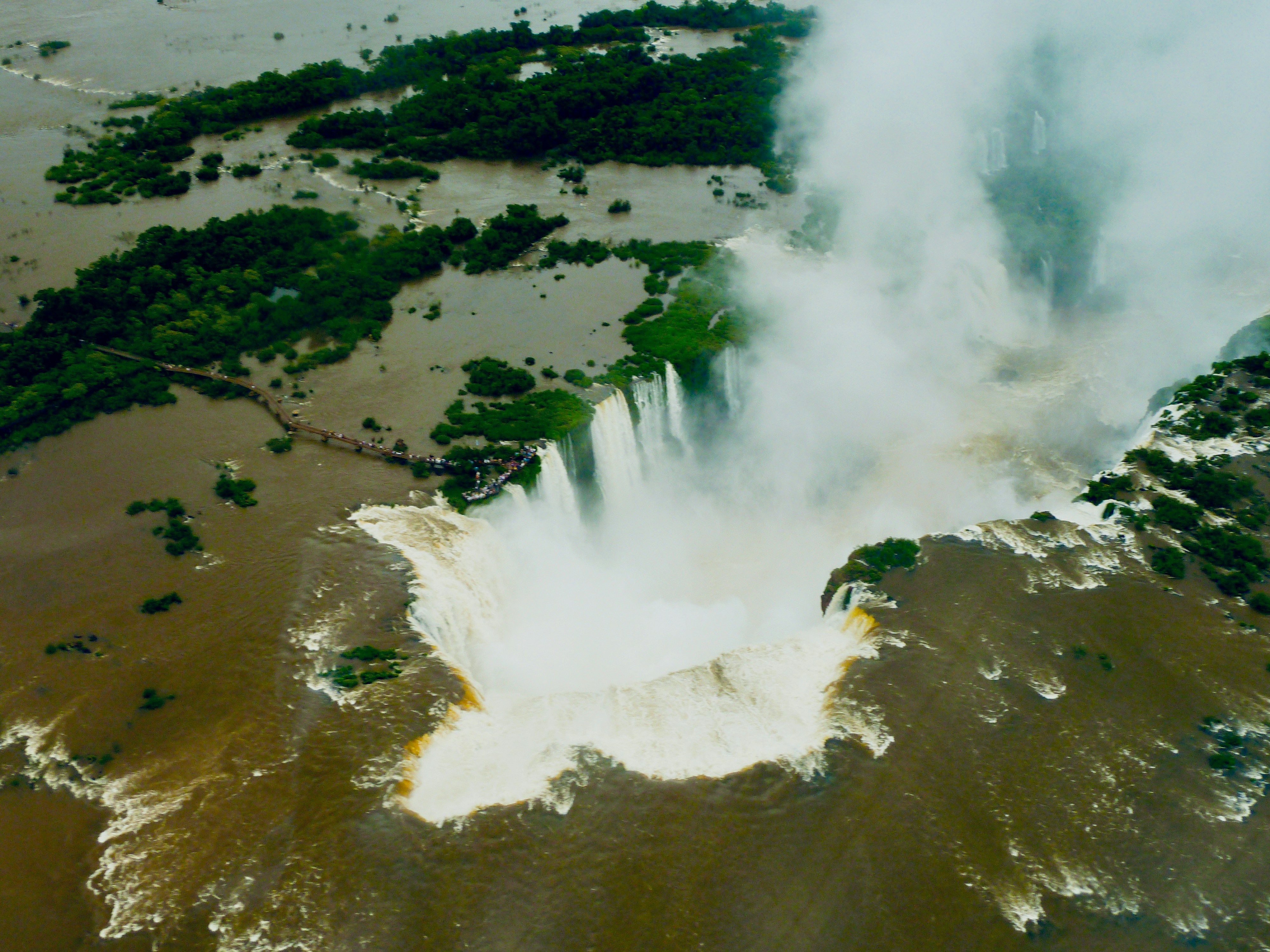 Aerial view of a waterfall cascading into a river surrounded by lush greenery.