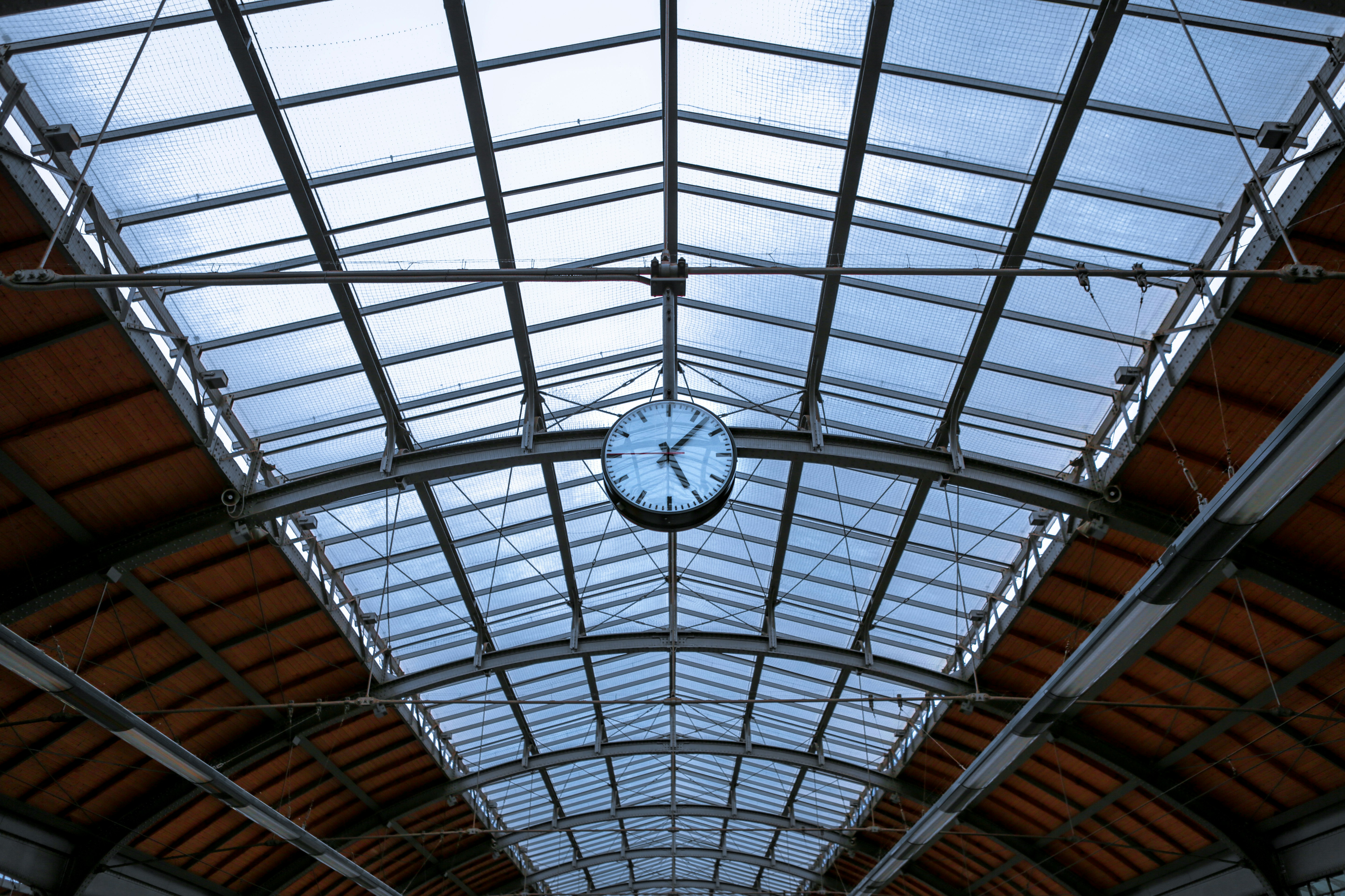 A large clock suspended from a glass and metal ceiling, showcasing the intricate design of the station's architecture.