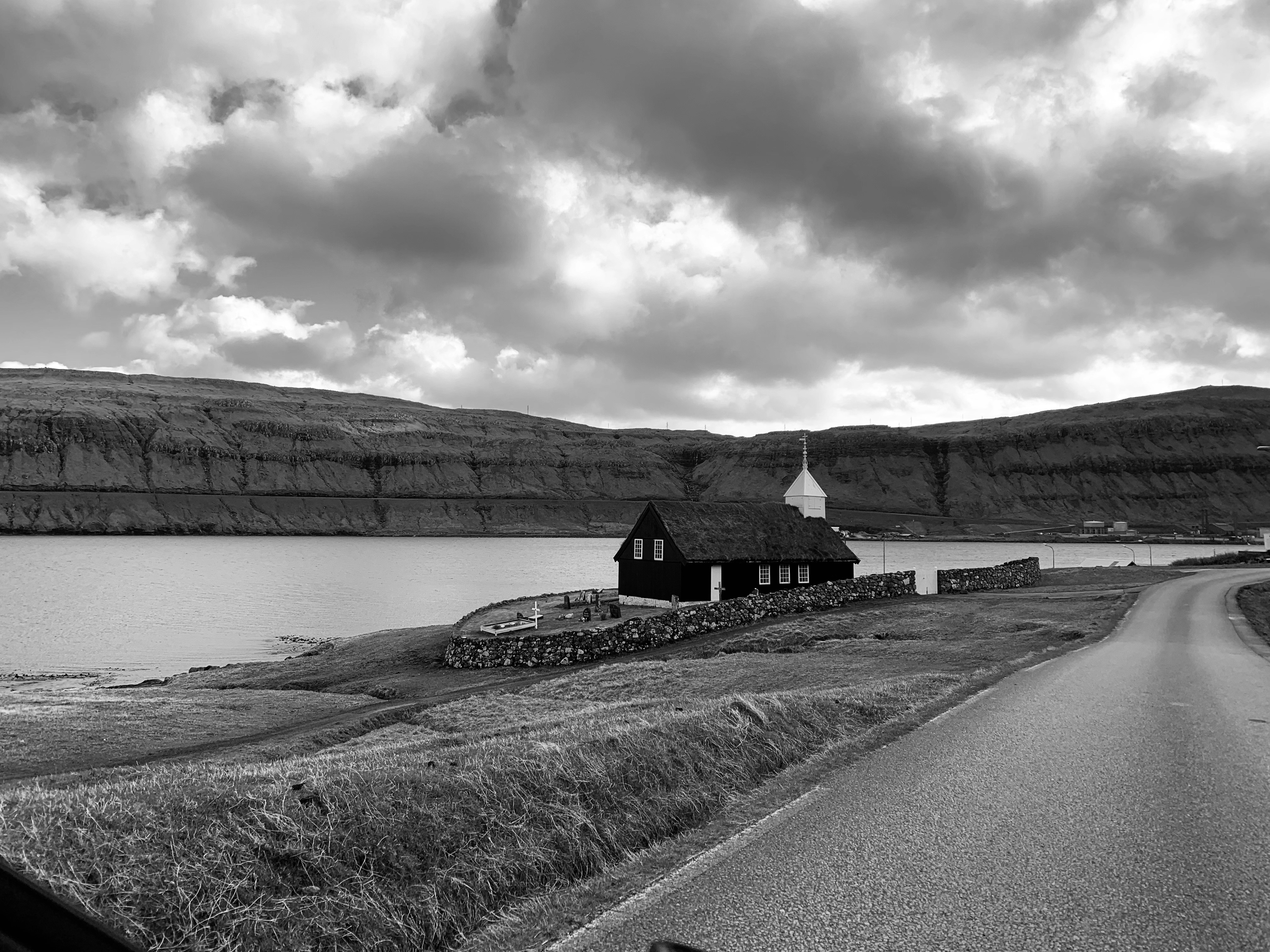 Black cabin nestled by a serene river under a dramatic cloudy sky.