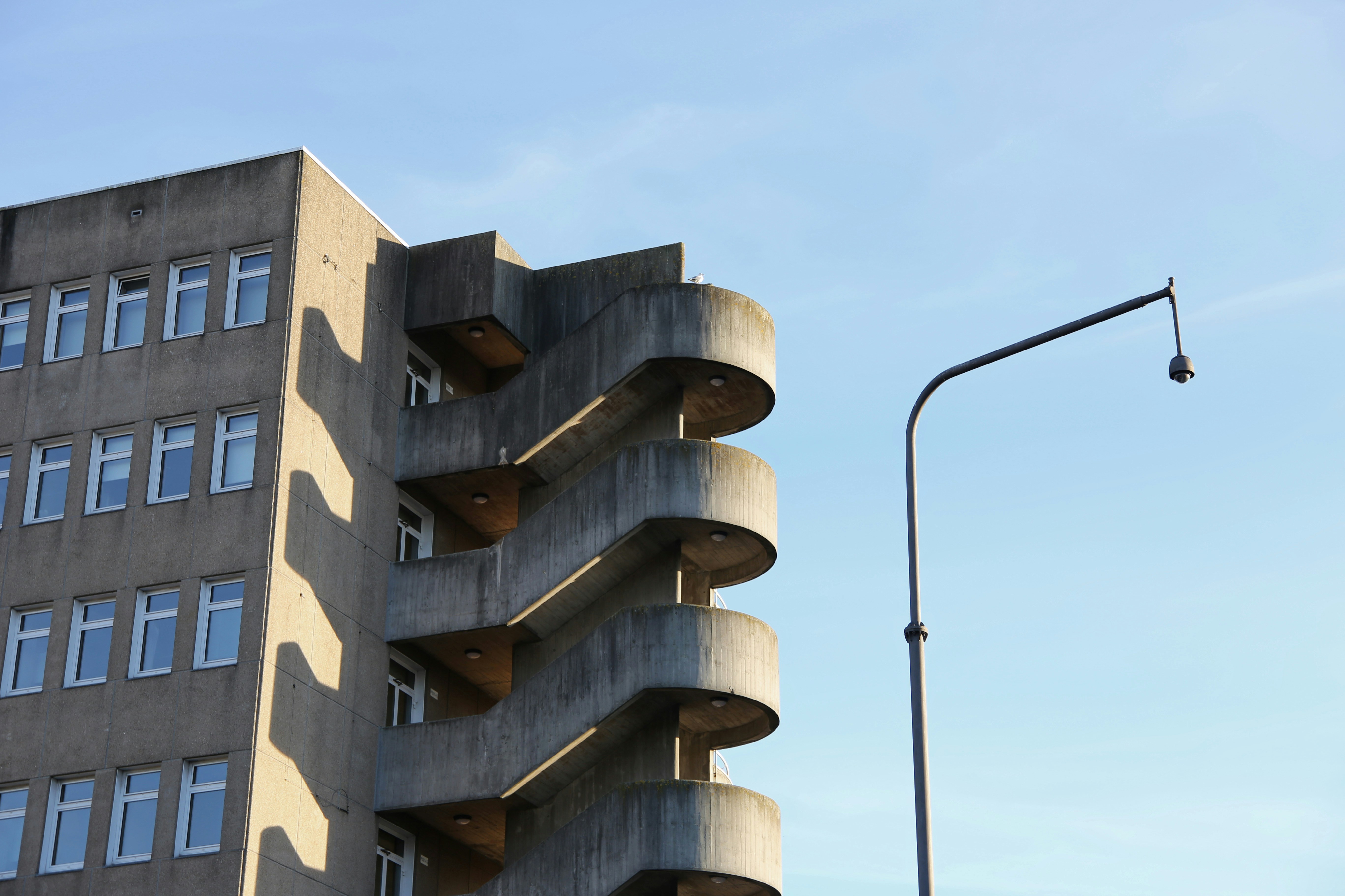 Concrete spiral staircase attached to a building, showcasing geometric design against a clear blue sky.