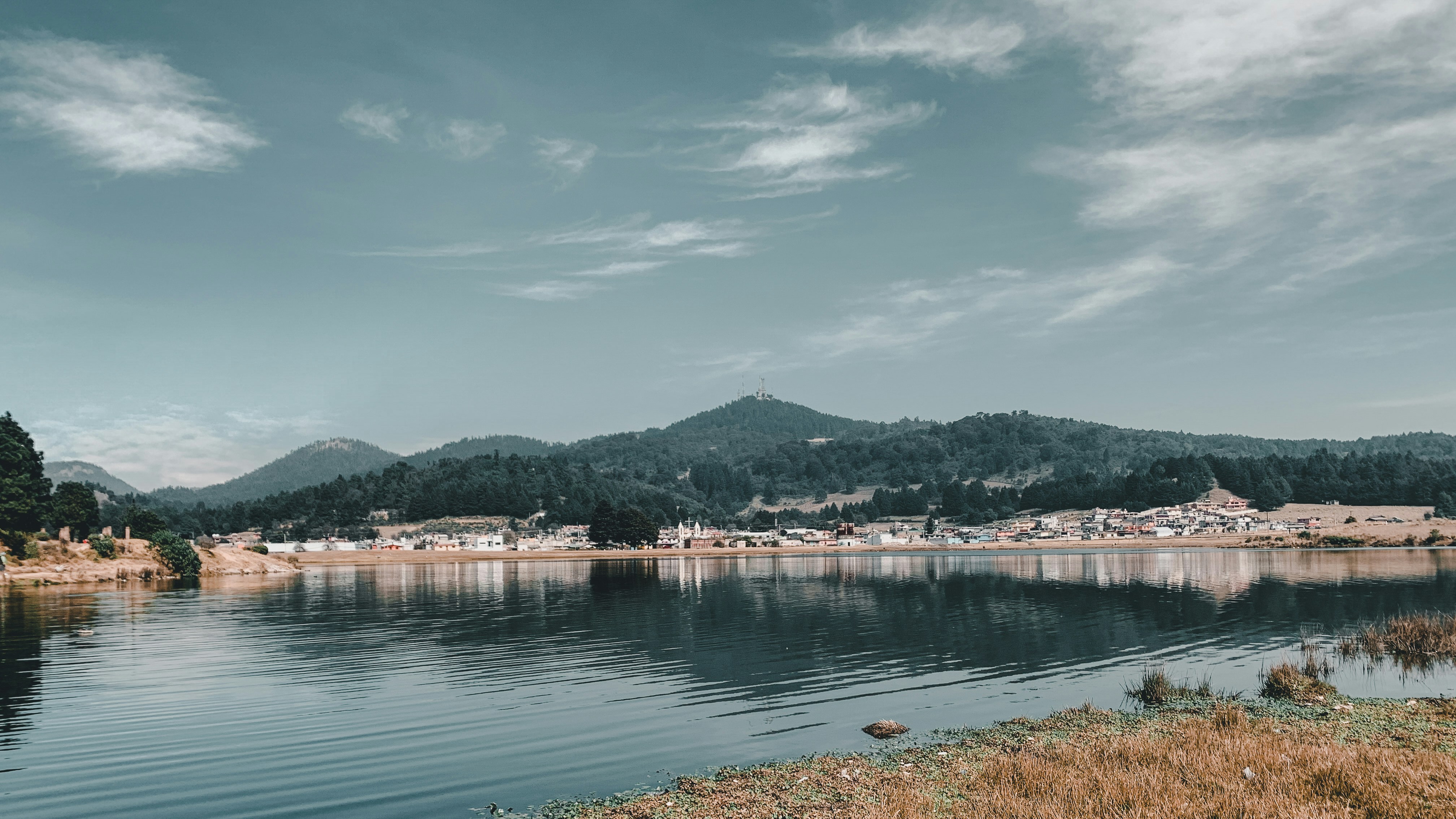 Serene lake reflecting a line of quaint houses and distant mountains under a partly cloudy sky.