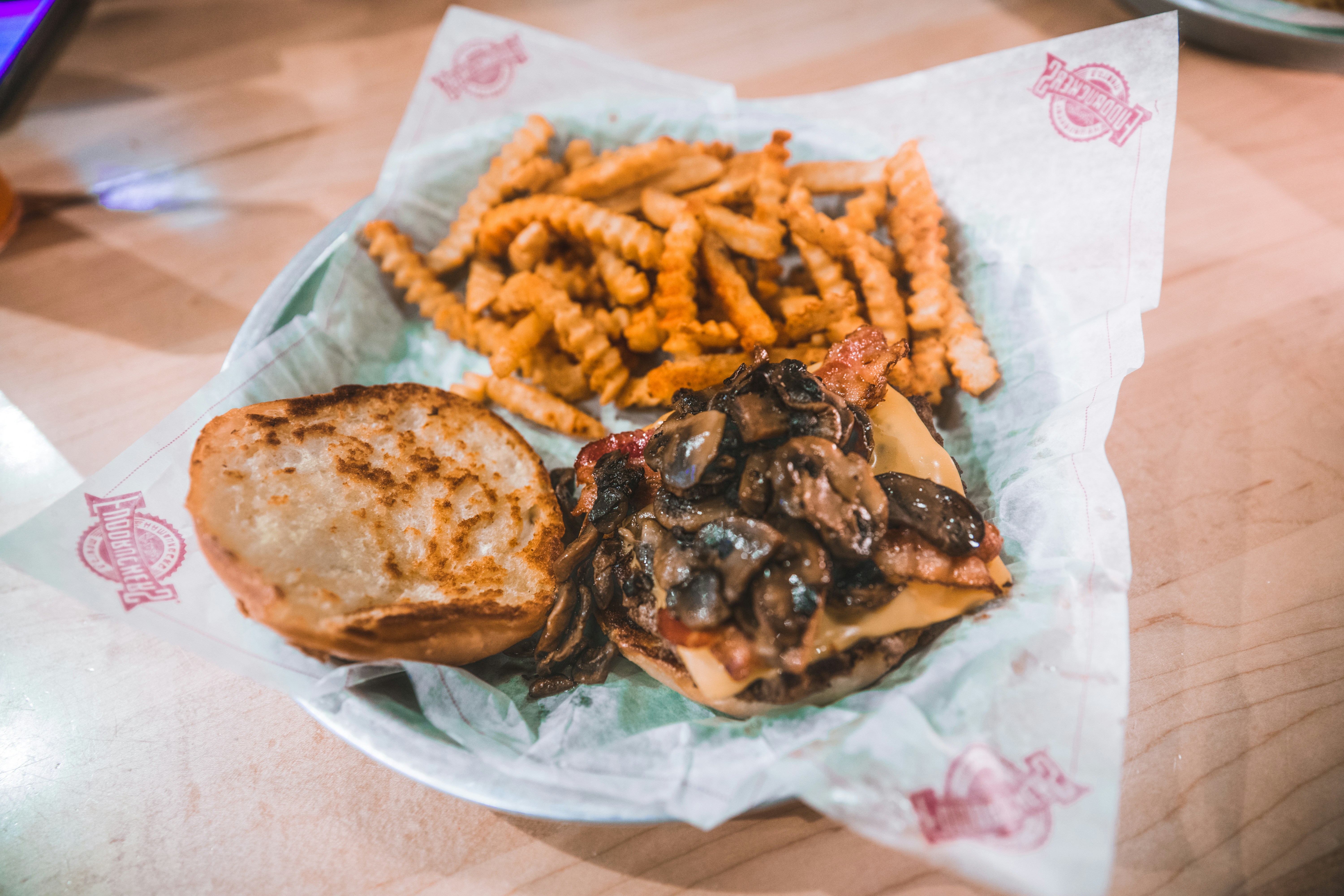 Burger topped with sautéed mushrooms and Swiss cheese alongside crinkle-cut fries on a plate.