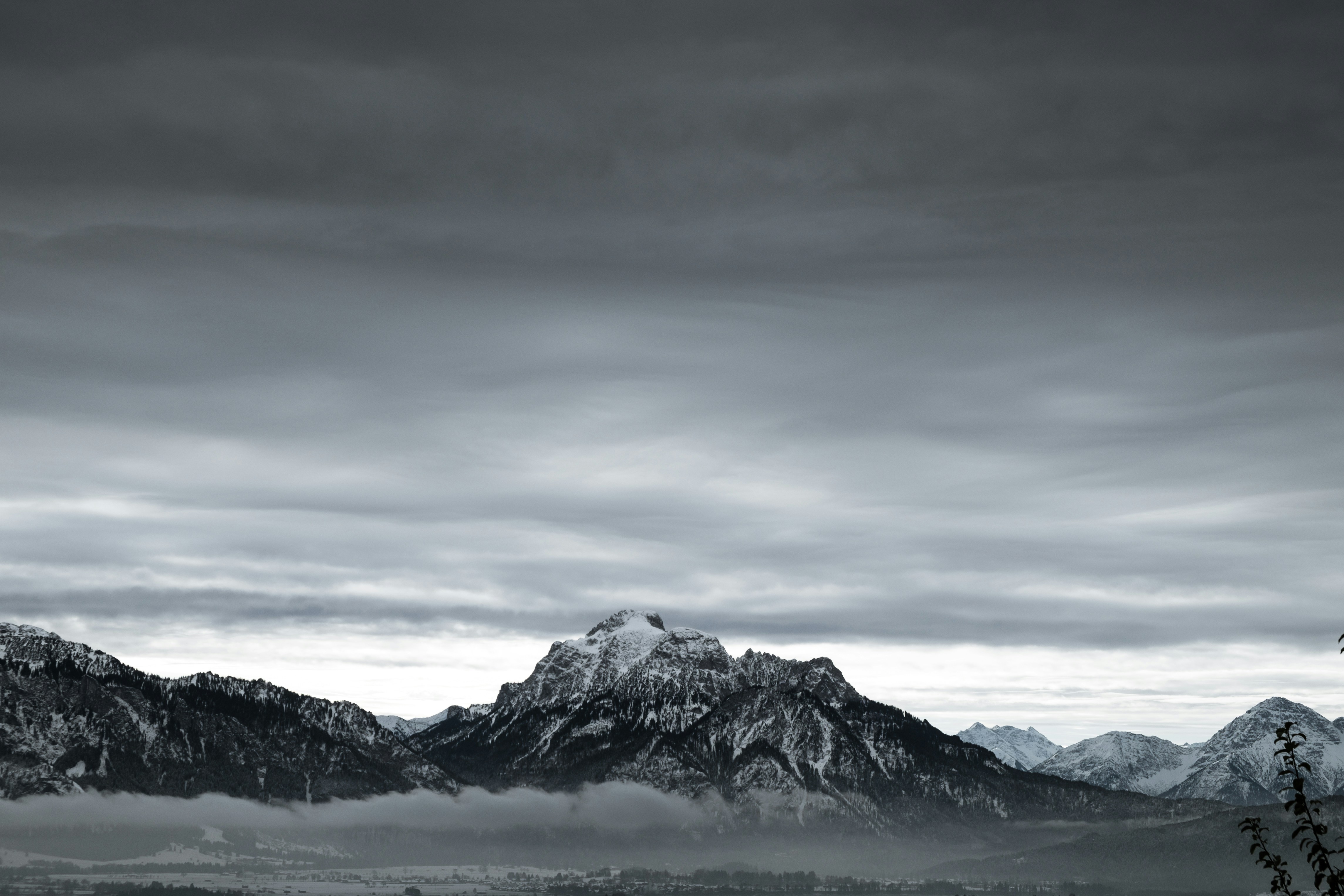 Dramatic mountain range shrouded in clouds, showcasing rugged peaks dusted with snow. The monochromatic palette emphasizes the stark beauty of the landscape.