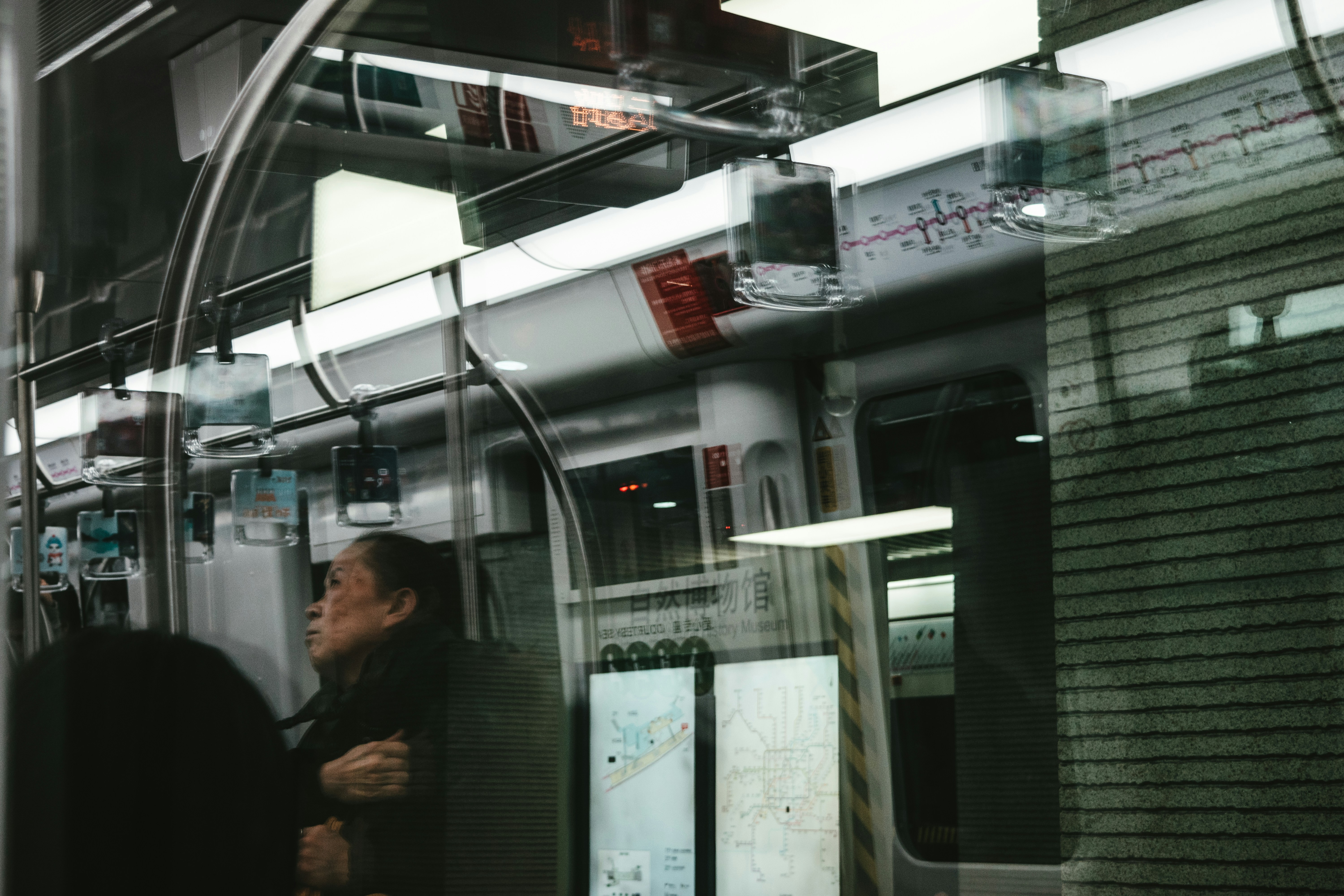 Interior of a subway train featuring reflections of passengers and transit maps on glass surfaces.