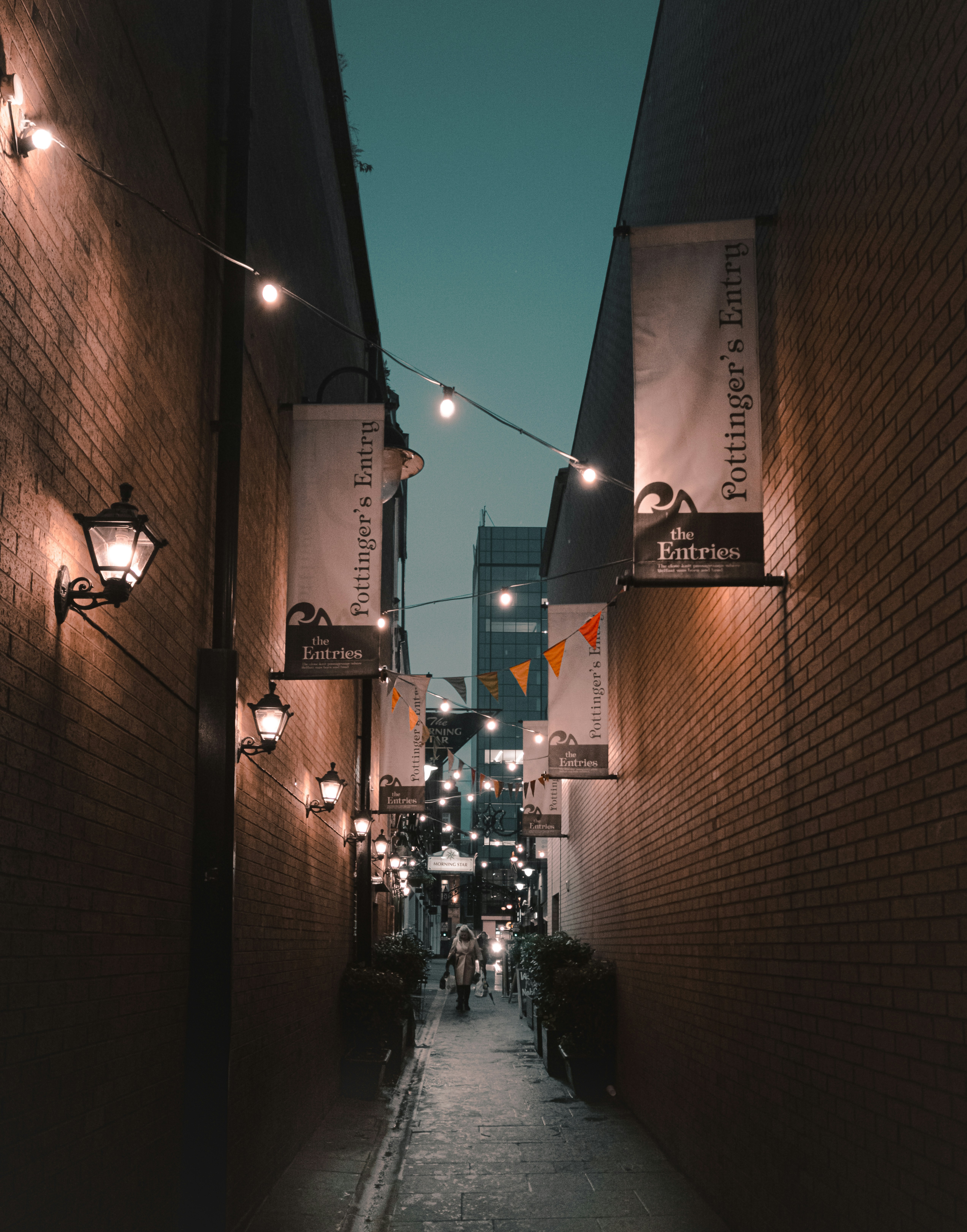 Person walking on street between buildings with string light on toabove ...