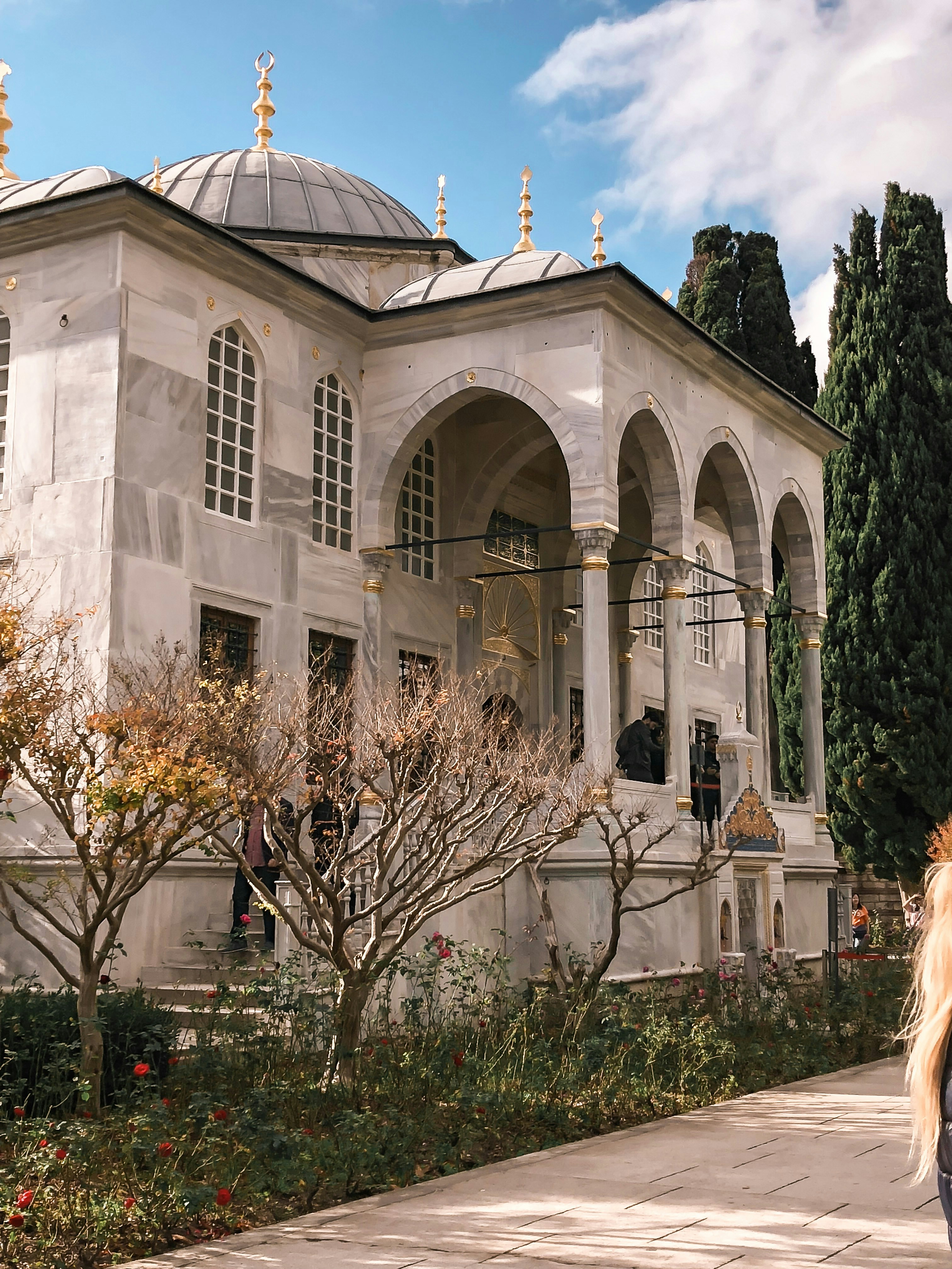 Intricately designed building showcasing arched windows and ornate details, surrounded by lush greenery and blooming flowers.