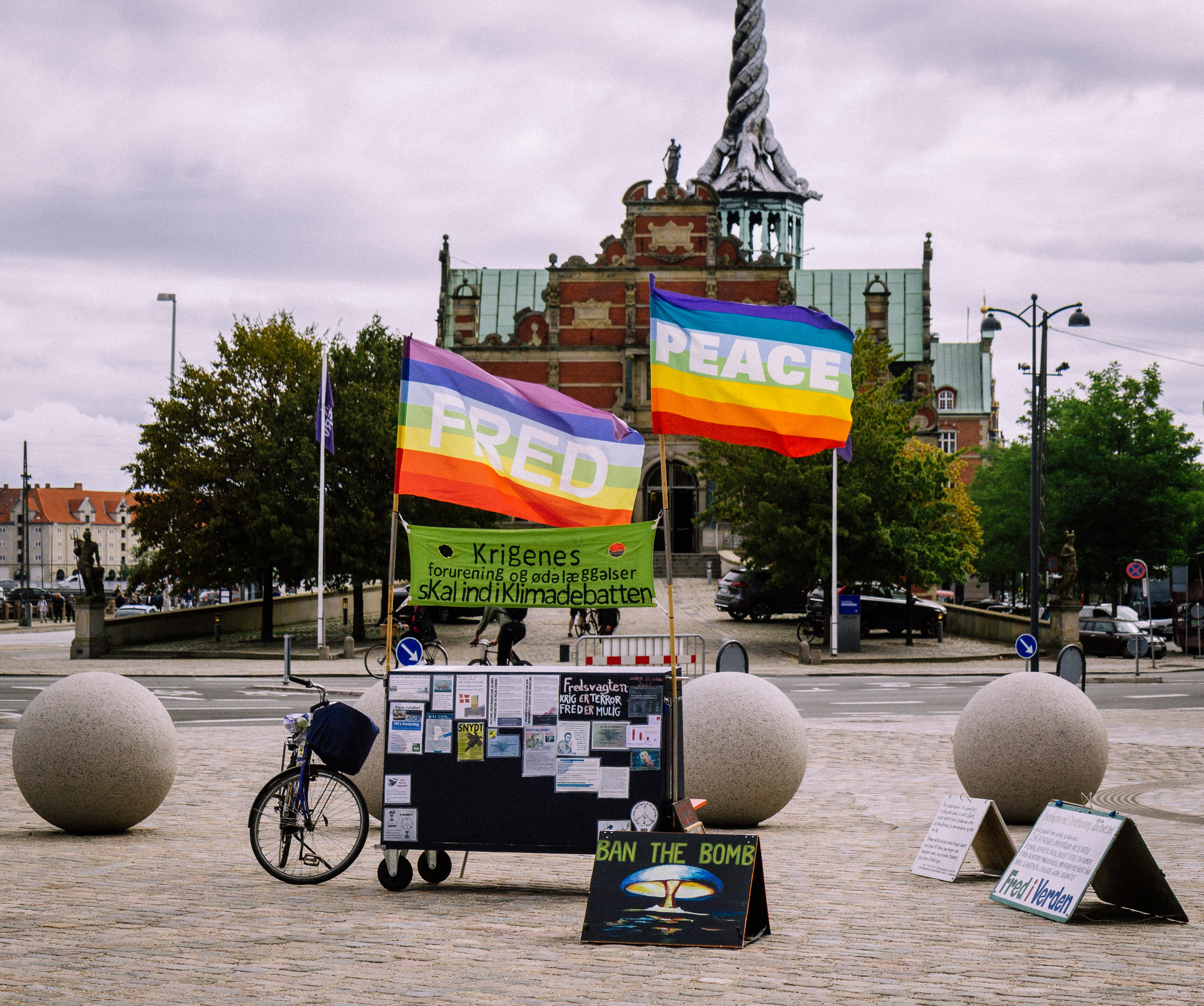 Colorful flags proclaiming peace and anti-nuclear sentiments at a public demonstration, with a bicycle and informational displays in the foreground.