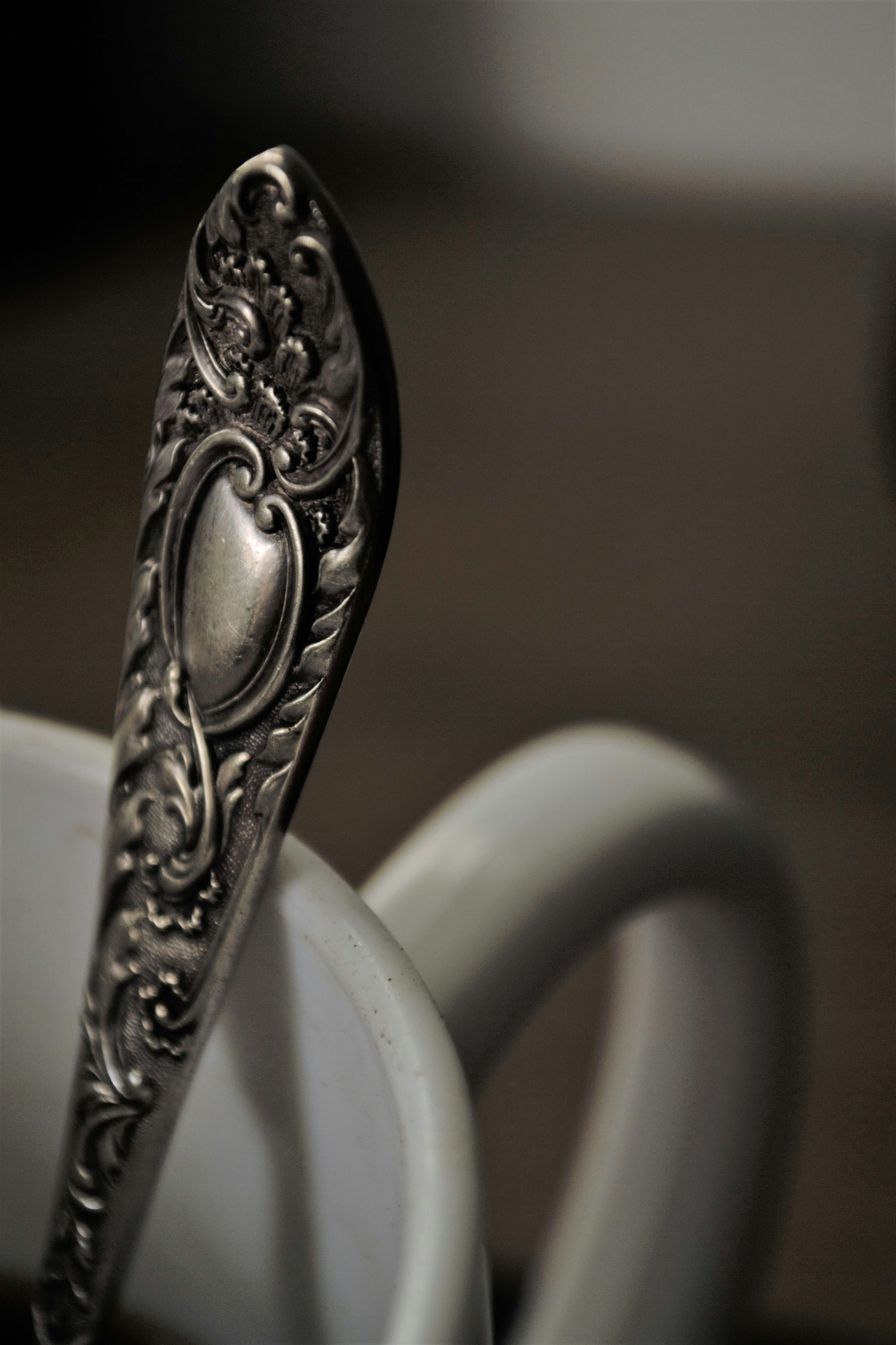 Intricately designed silver spoon resting within a white cup, highlighting its ornate details against a blurred background.