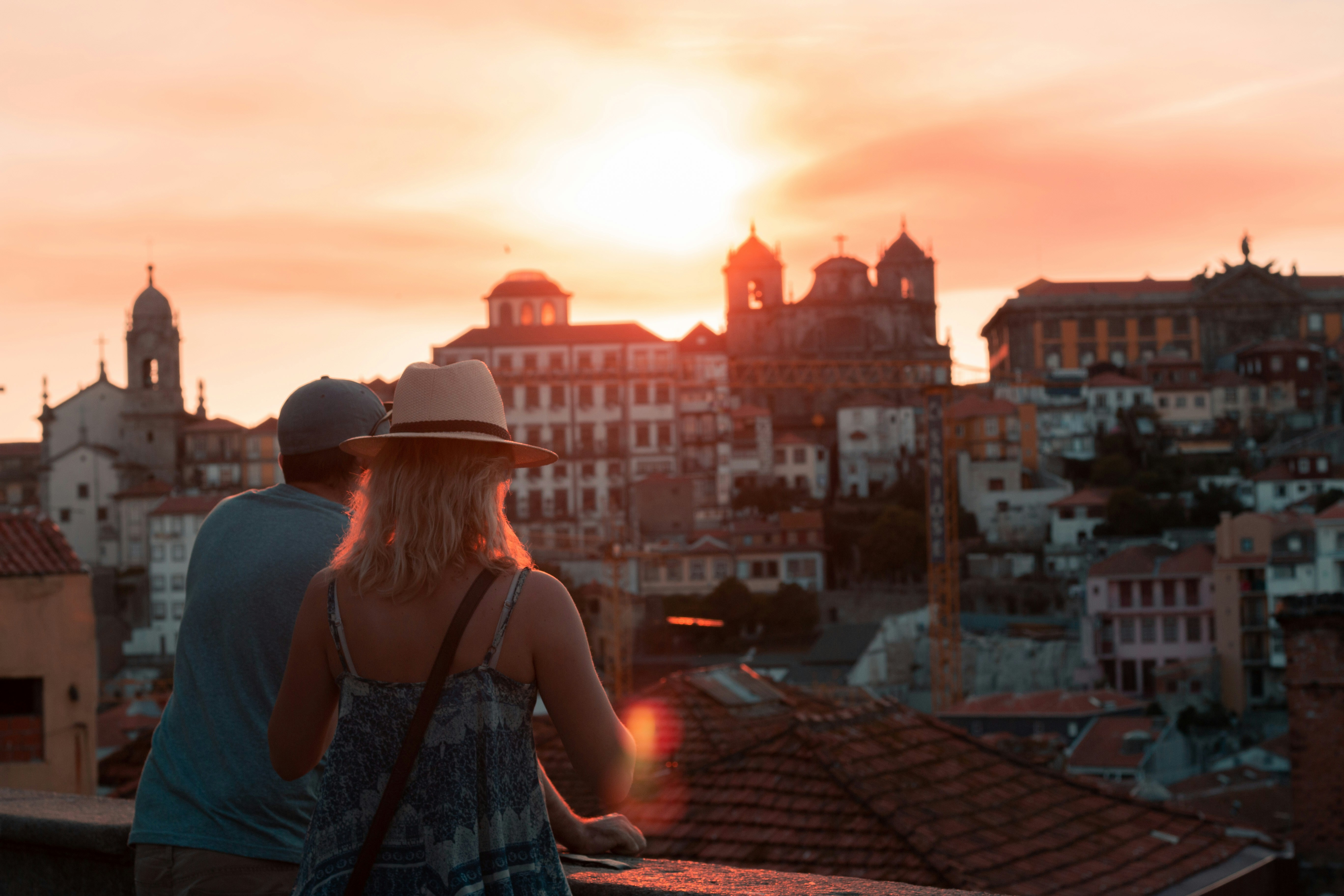 Two people stand on a rooftop terrace overlooking a cityscape at sunset.