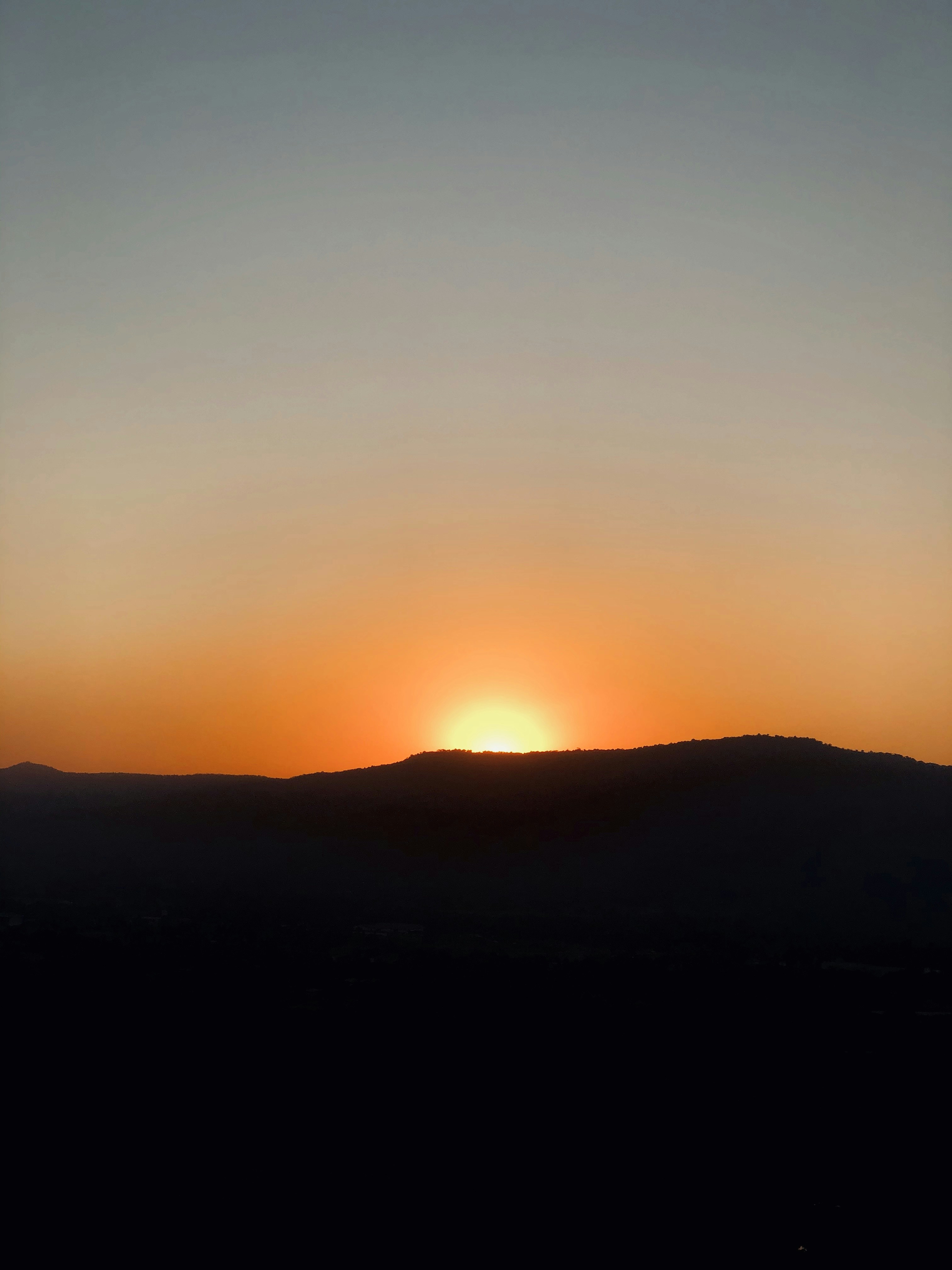 Golden sun rising above distant mountains, casting a warm glow across the sky. The gradient of colors transitions from orange to blue.