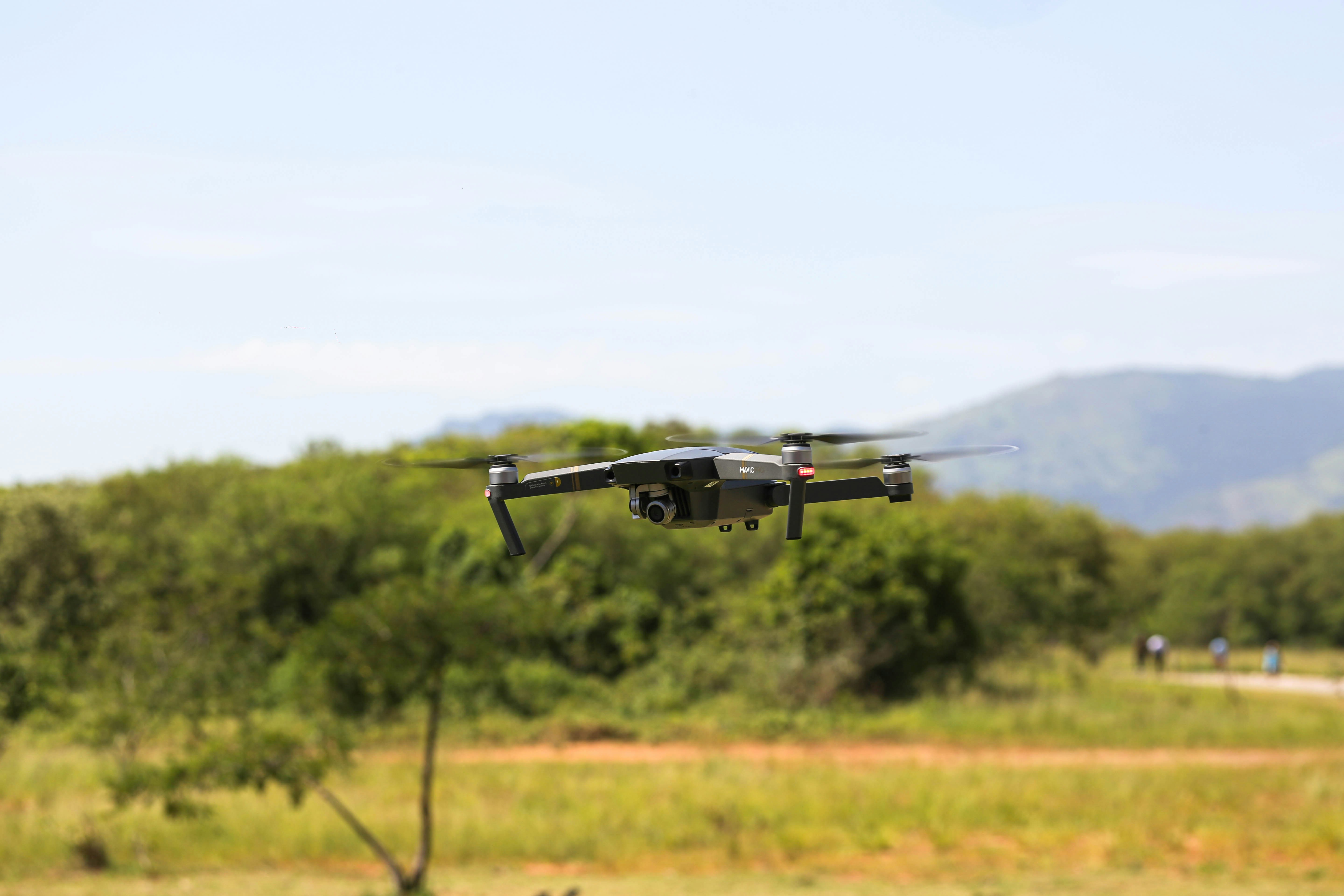Drone flying low above a grassy field with distant mountains under a clear sky.