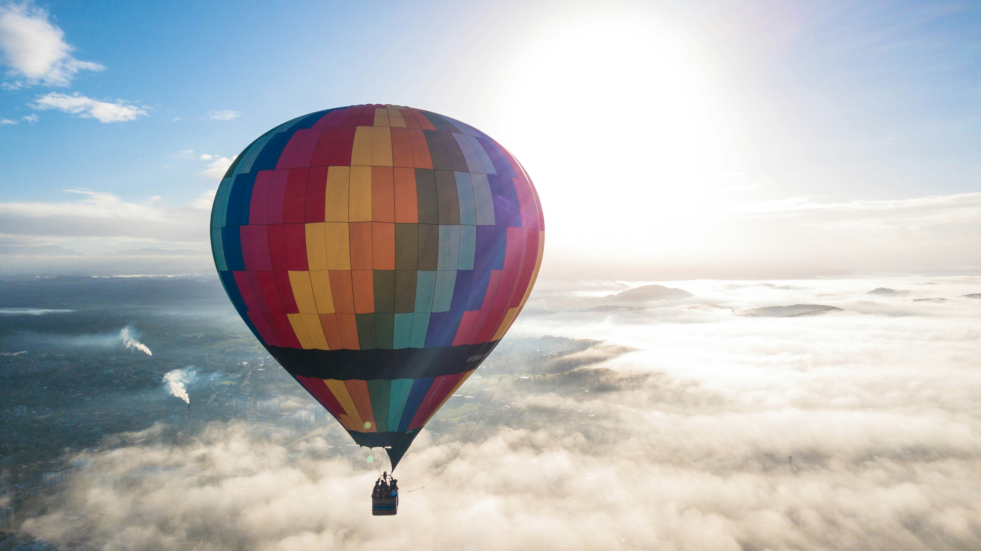 Multicolored hot air balloon soaring over a sunlit sea of clouds.