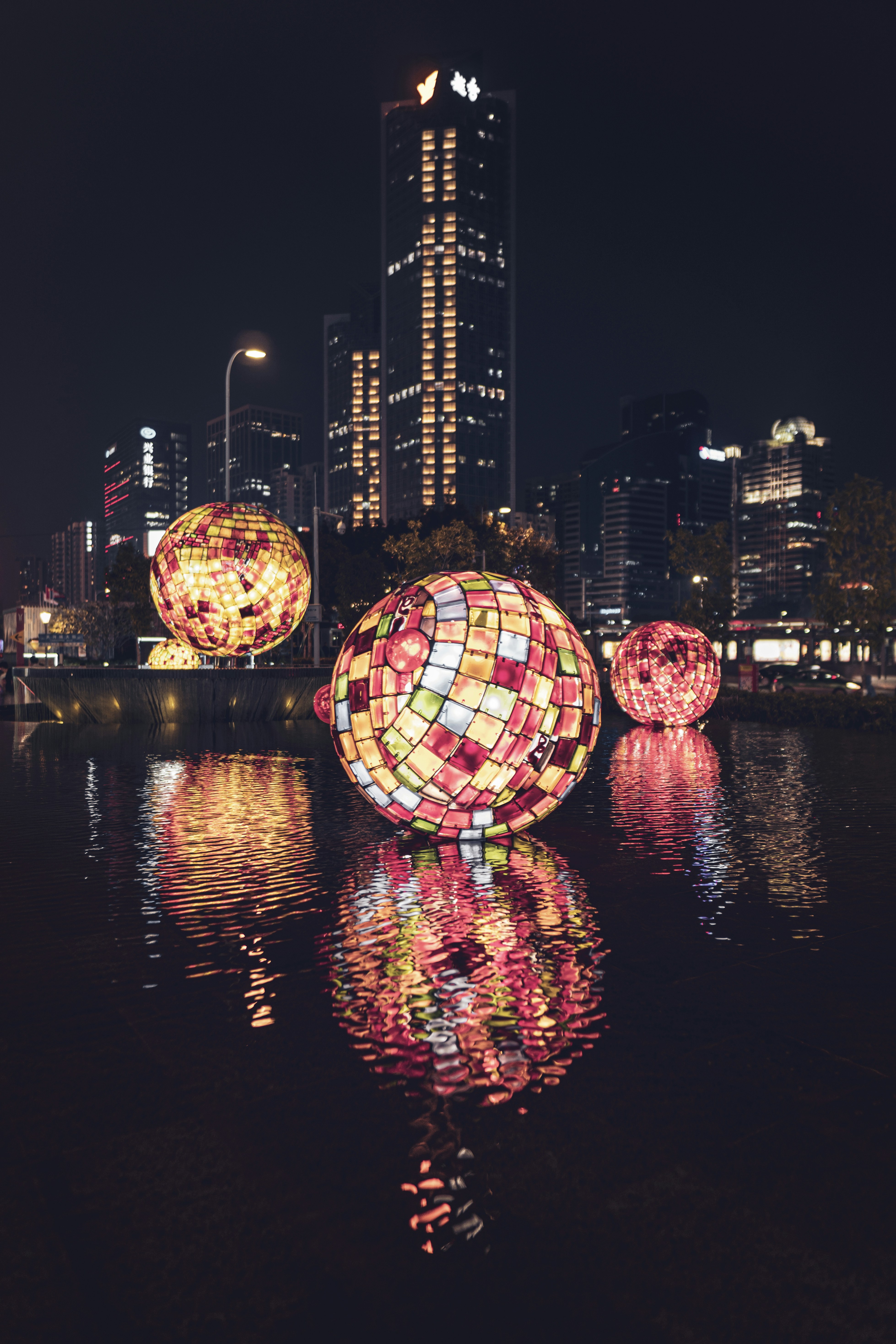 Colorful illuminated spheres float on water, reflecting the vibrant city skyline at night.