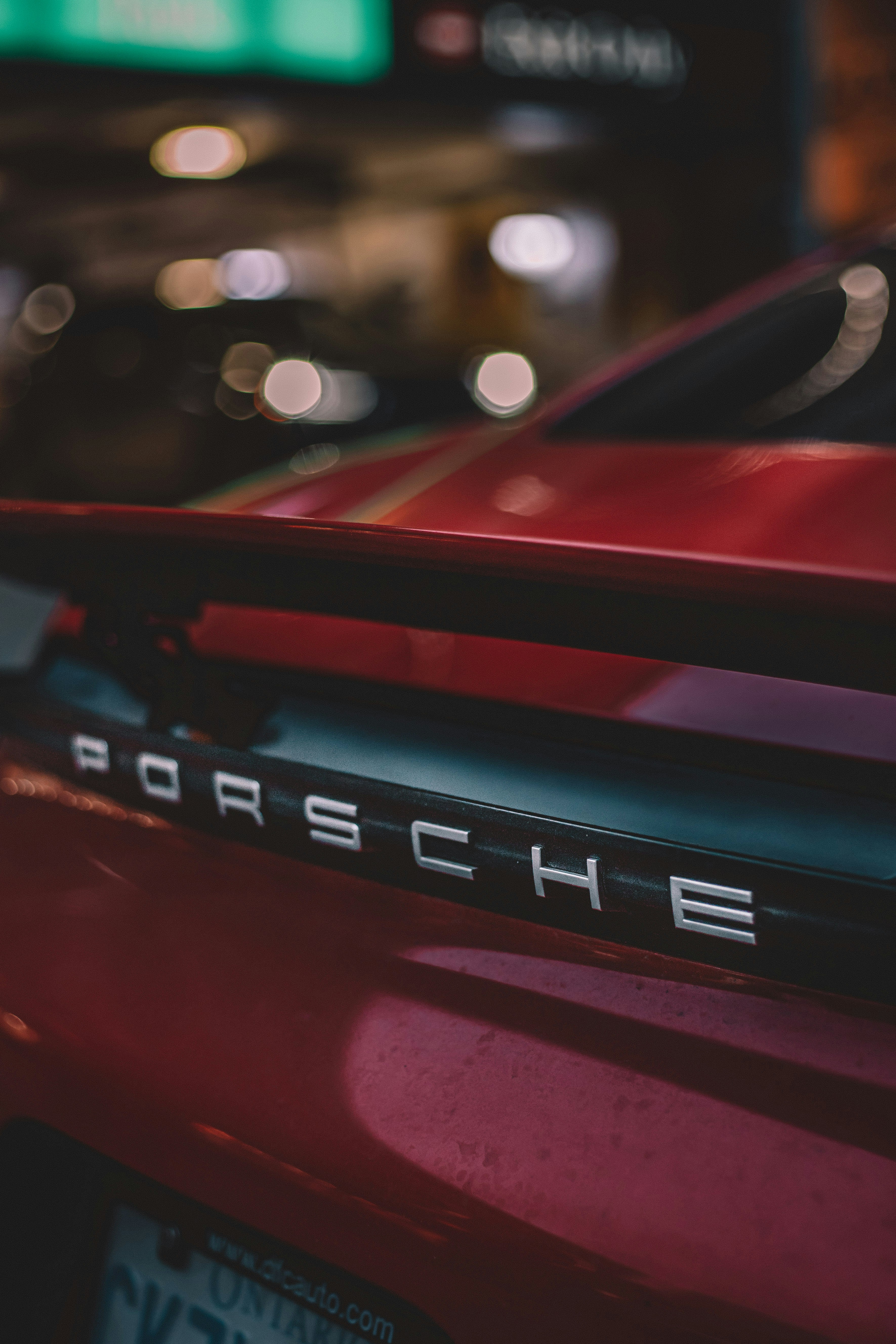Neon Night, Red Porsche: Focus on the Badge Amid City Blur
