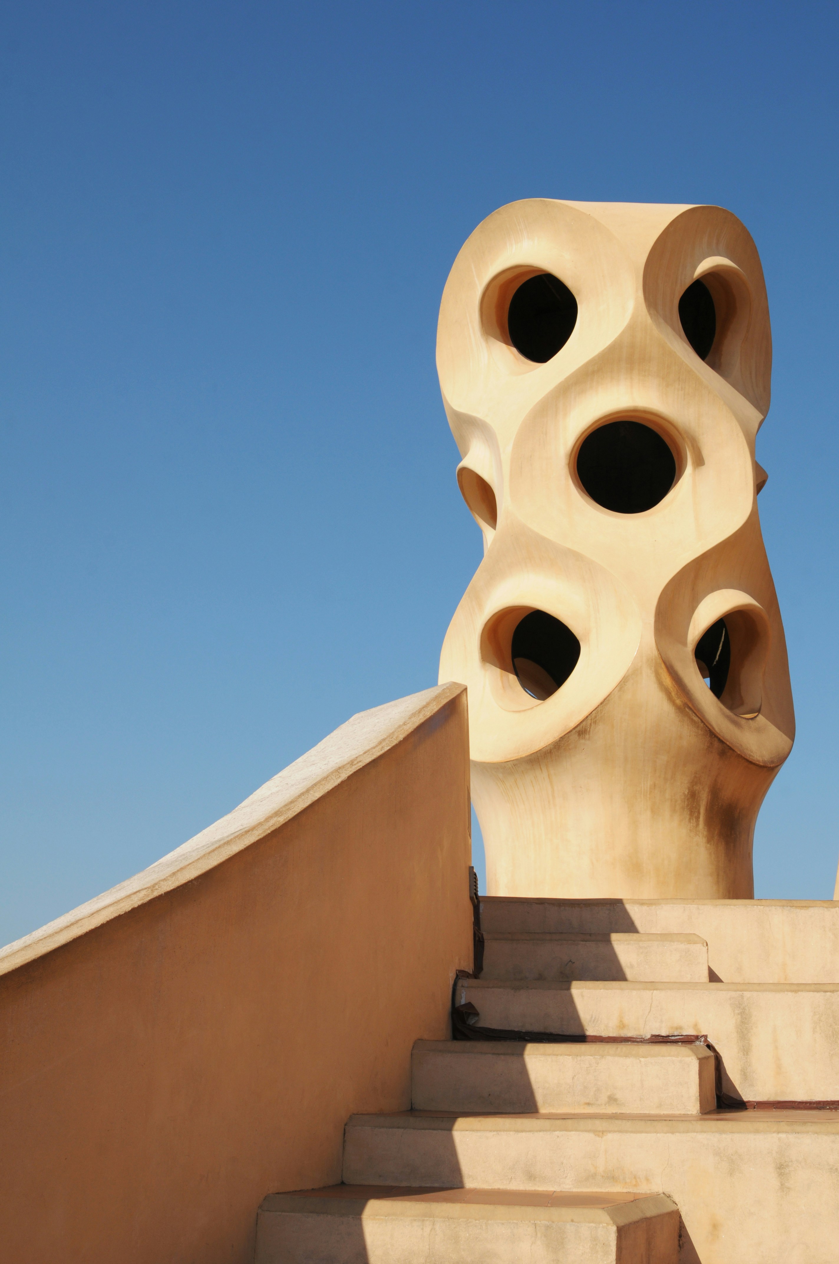 Whimsical architectural sculpture with rounded openings against a clear blue sky, leading the eye upward along a smooth staircase.