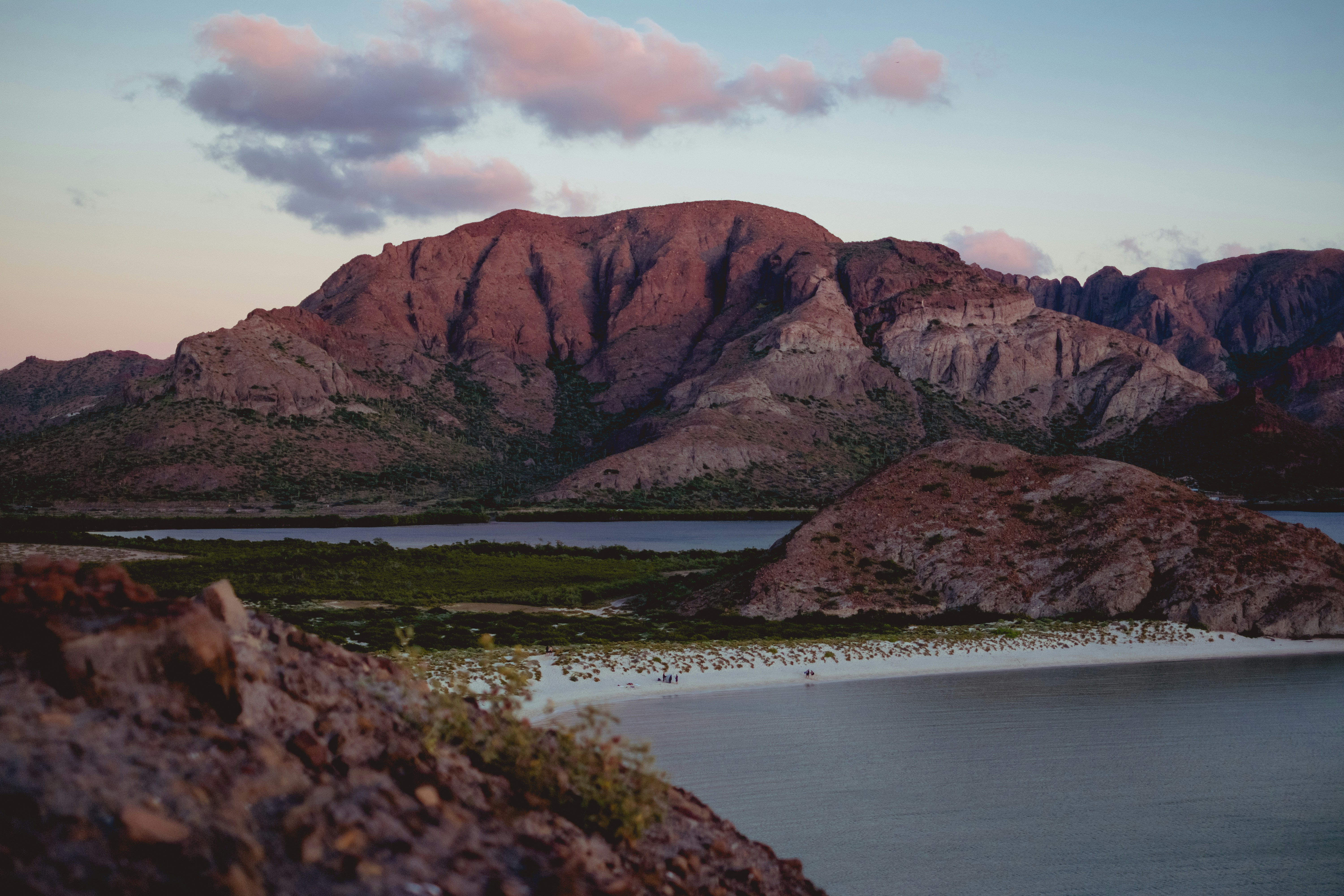 Dusky mountains bathed in warm sunset hues with a serene lake in the foreground.
