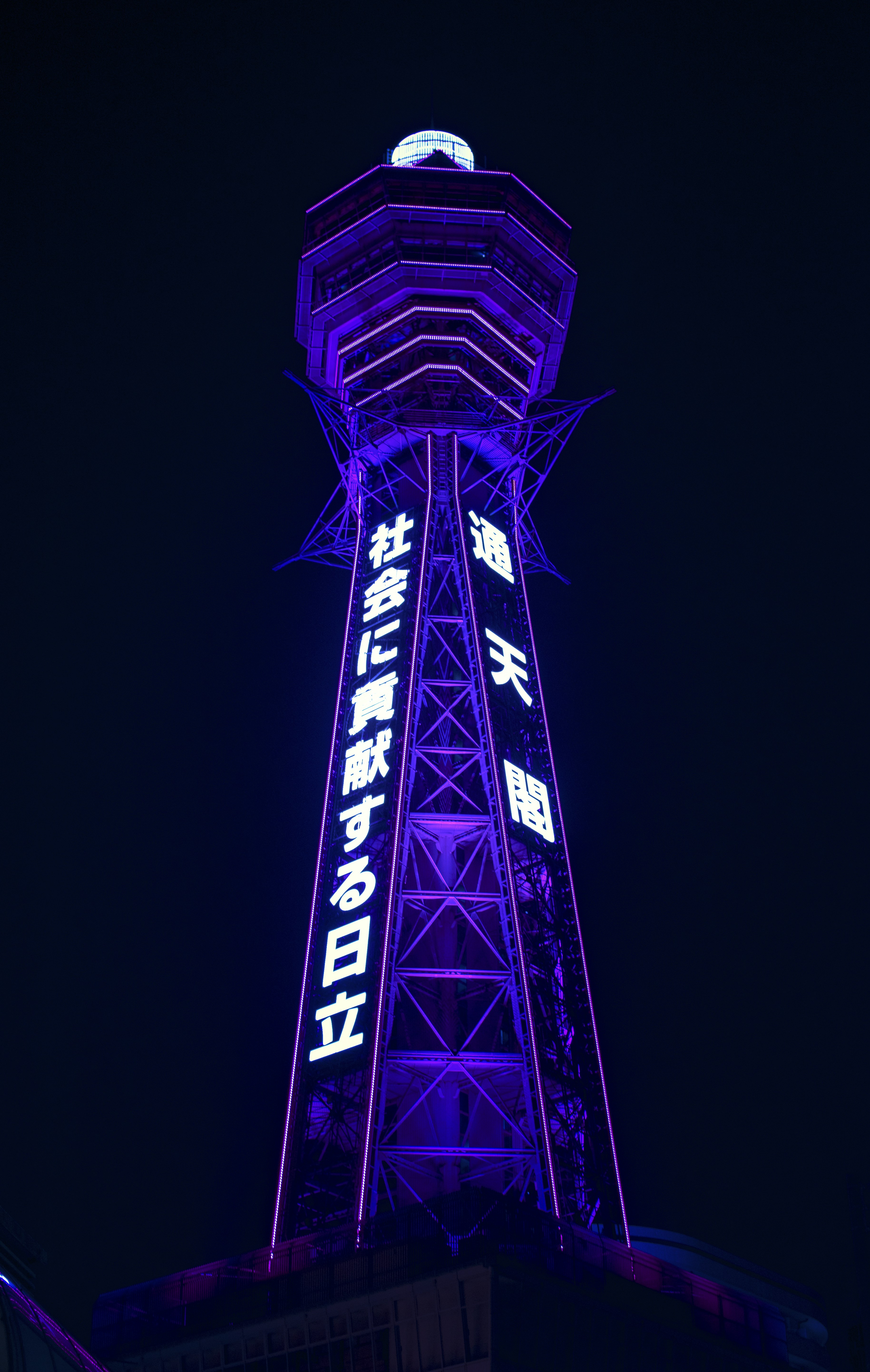 Tsuutenkaku Tower illuminated in vibrant purple neon against a night sky.