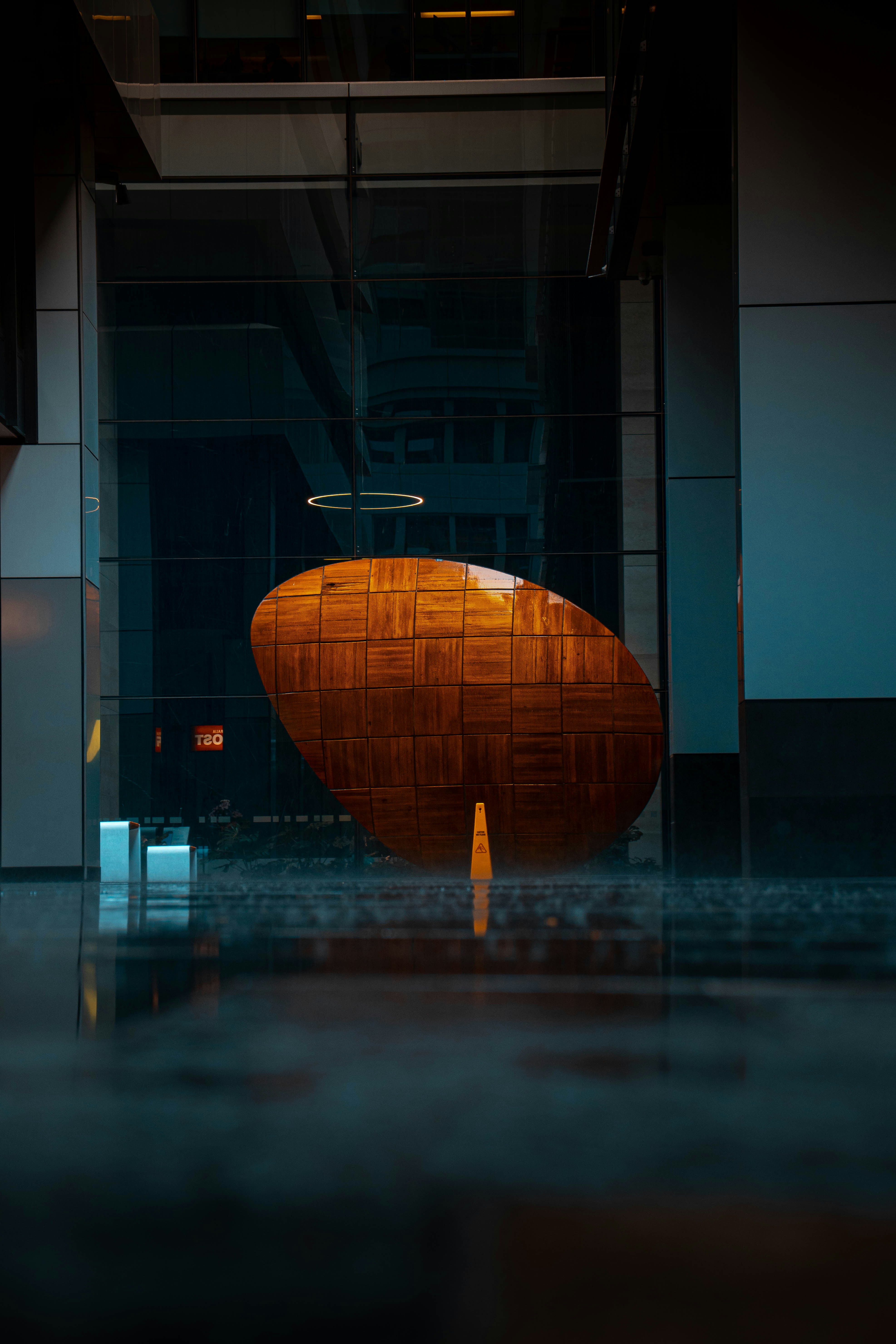 Copper Ellipse in a Glass Atrium: Warm Geometry Amid Neon Reflections