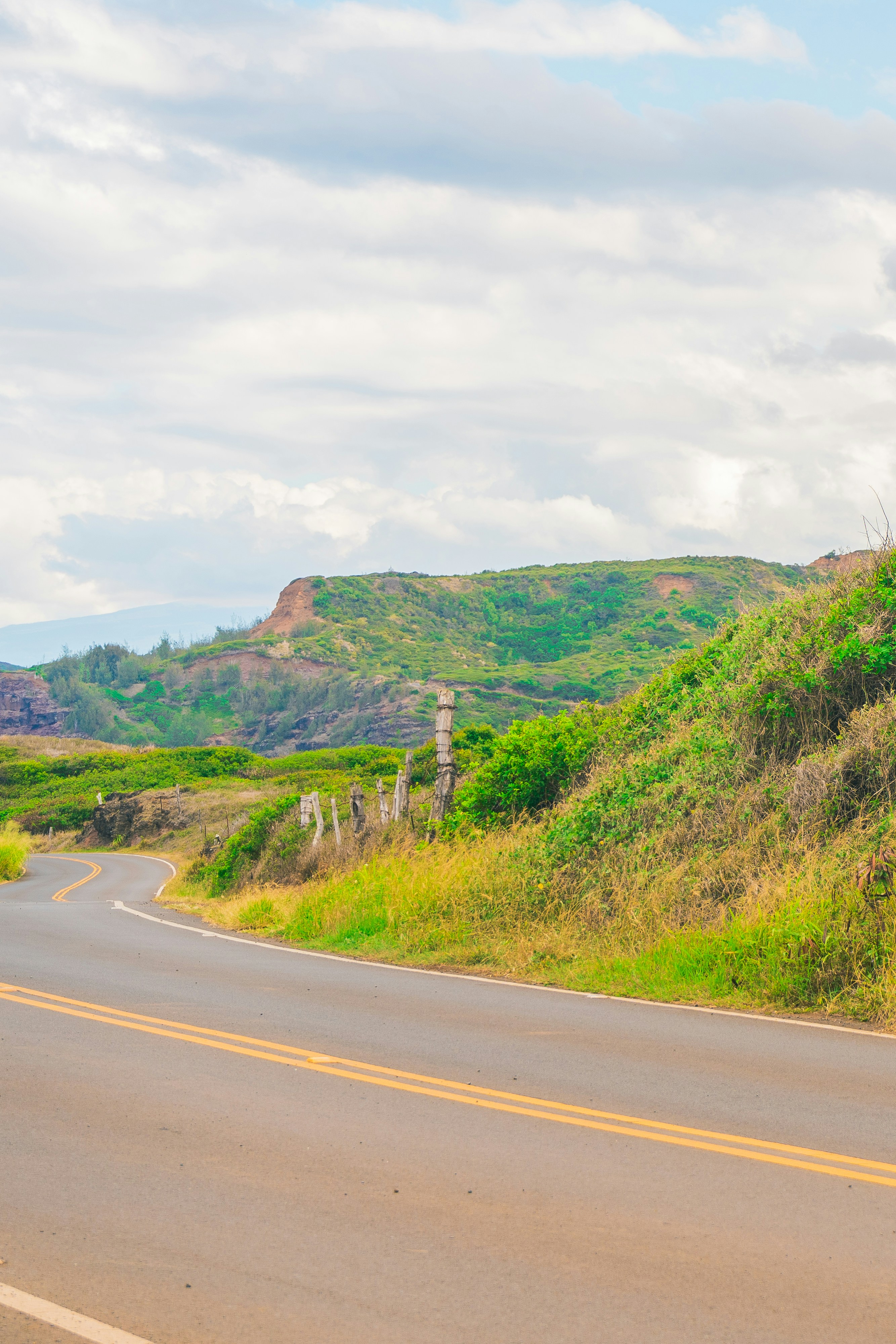 Winding Road Through Emerald Hills Beneath a Quiet Cloudscape