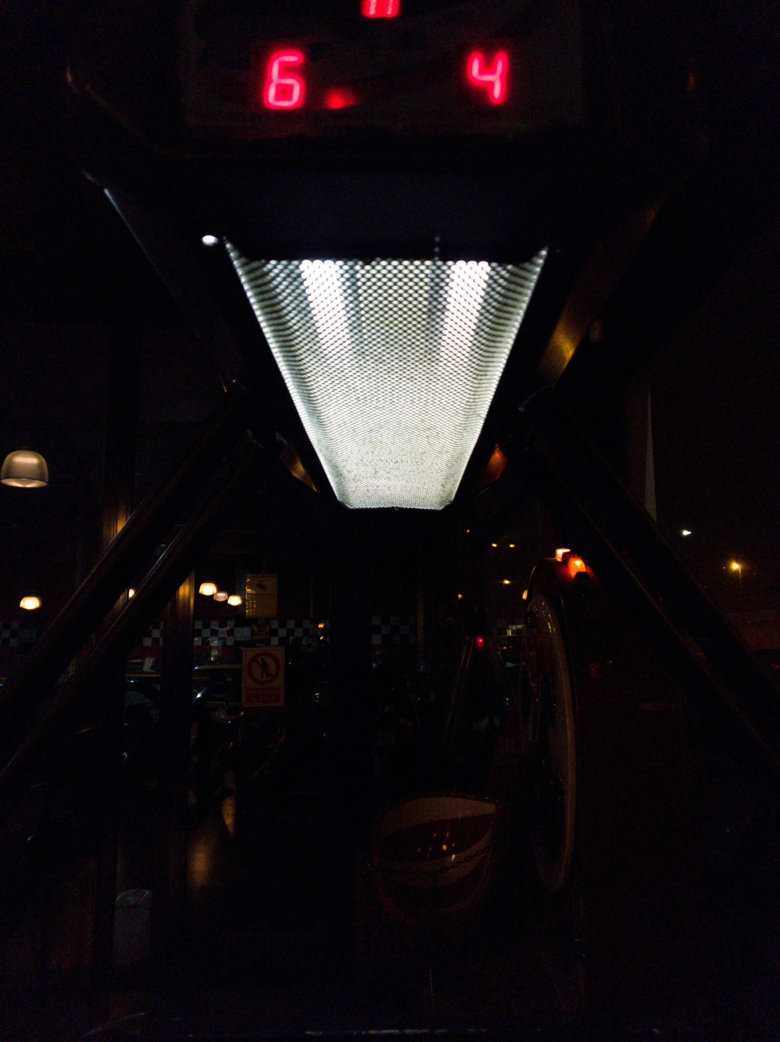 Bright overhead light fixture casting geometric patterns in a dimly lit diner setting.