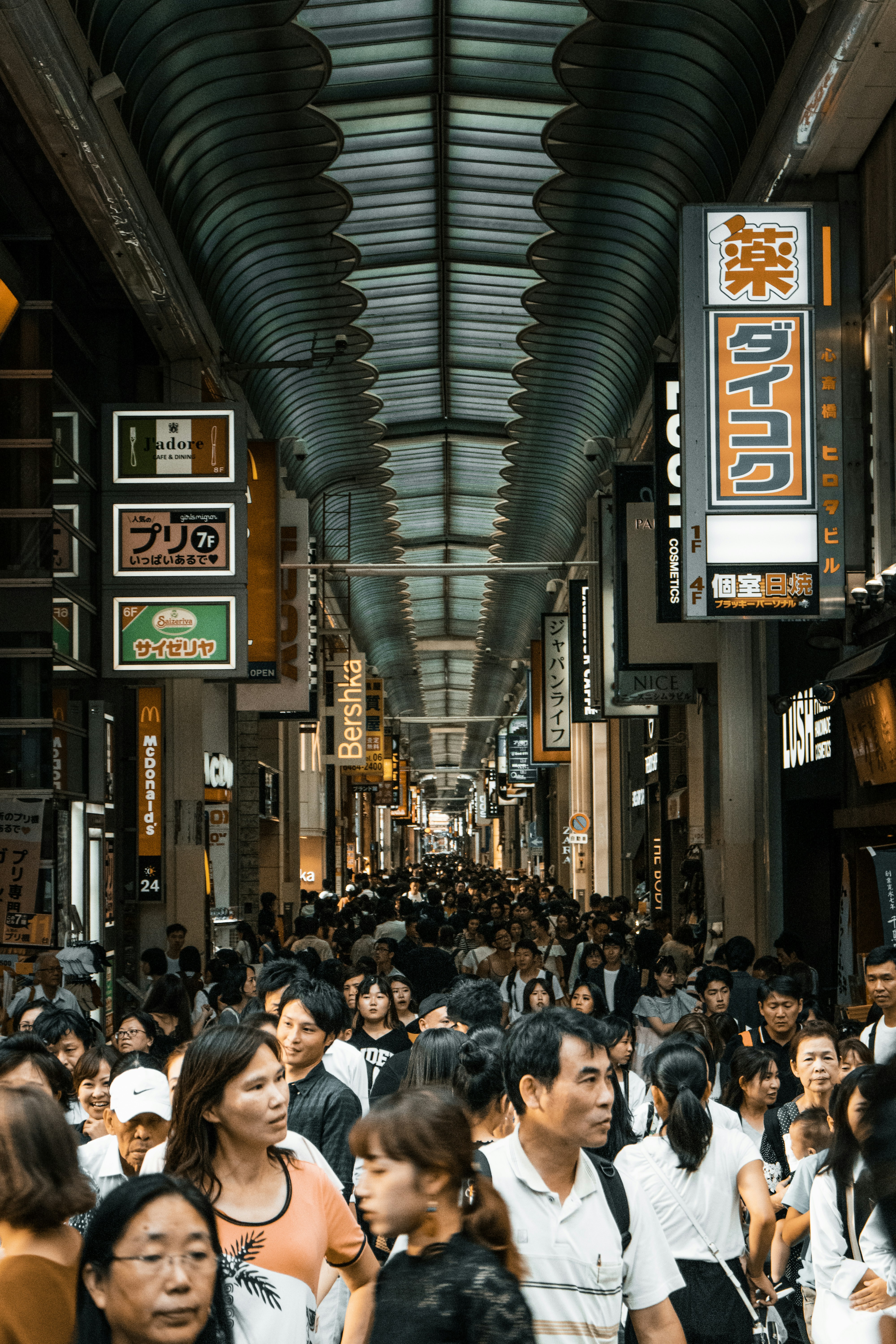 Bustling shopping street filled with diverse crowds and vibrant signage, showcasing urban life and commerce. The scene captures the essence of a lively city atmosphere.