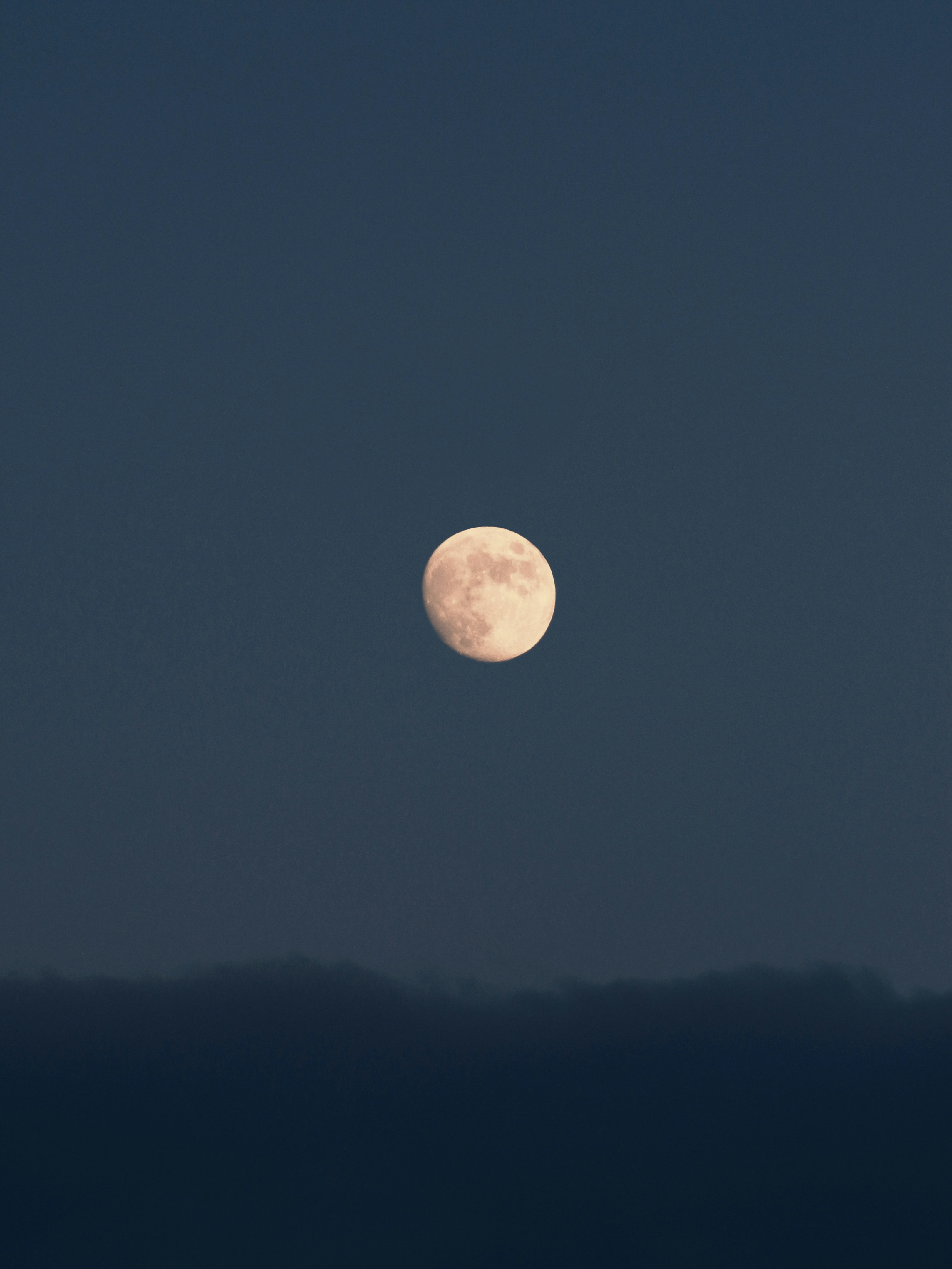 Full moon illuminating a dusky sky above darkened clouds.