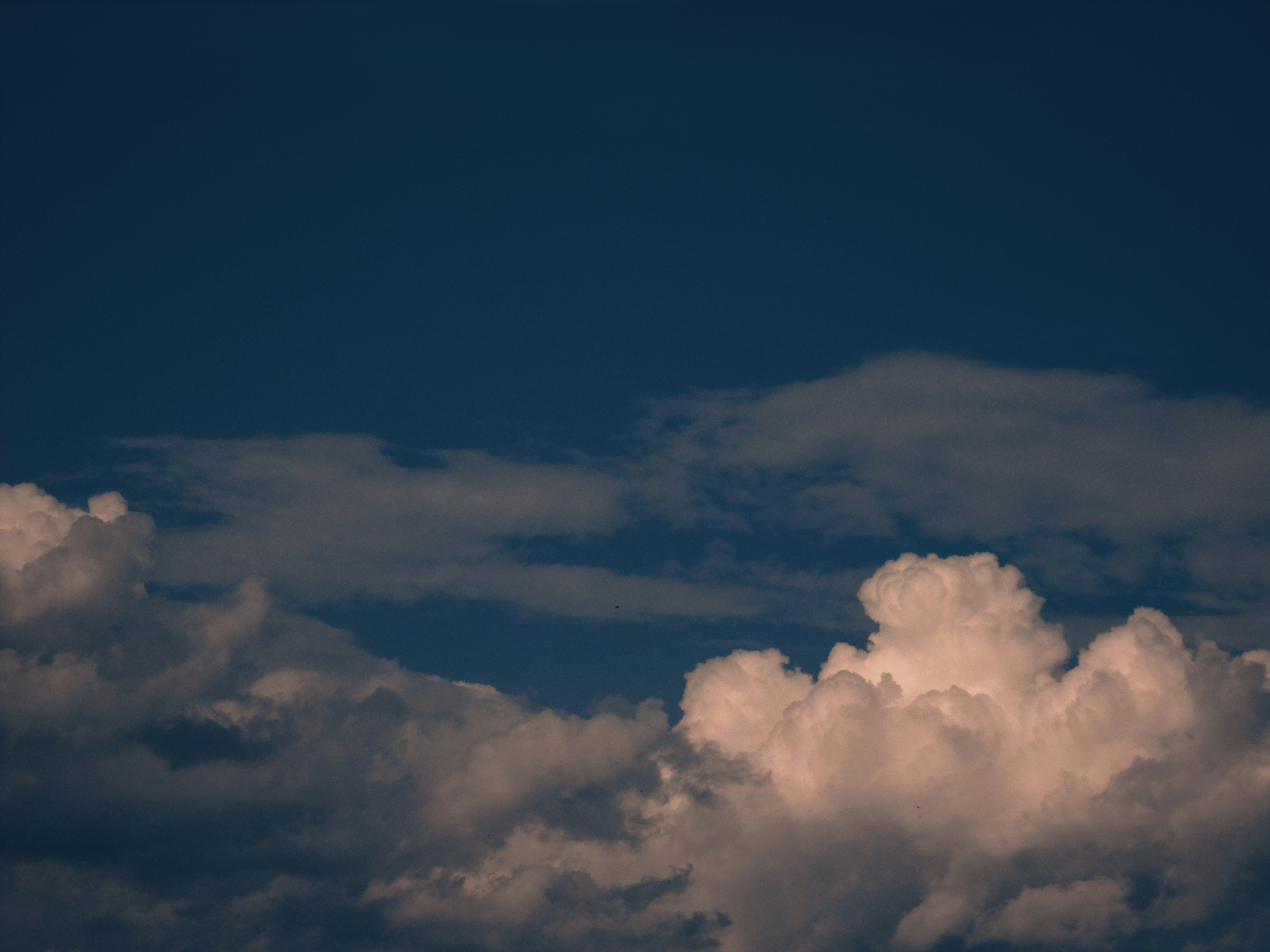 Dramatic clouds illuminated by soft evening light against a deep blue sky.