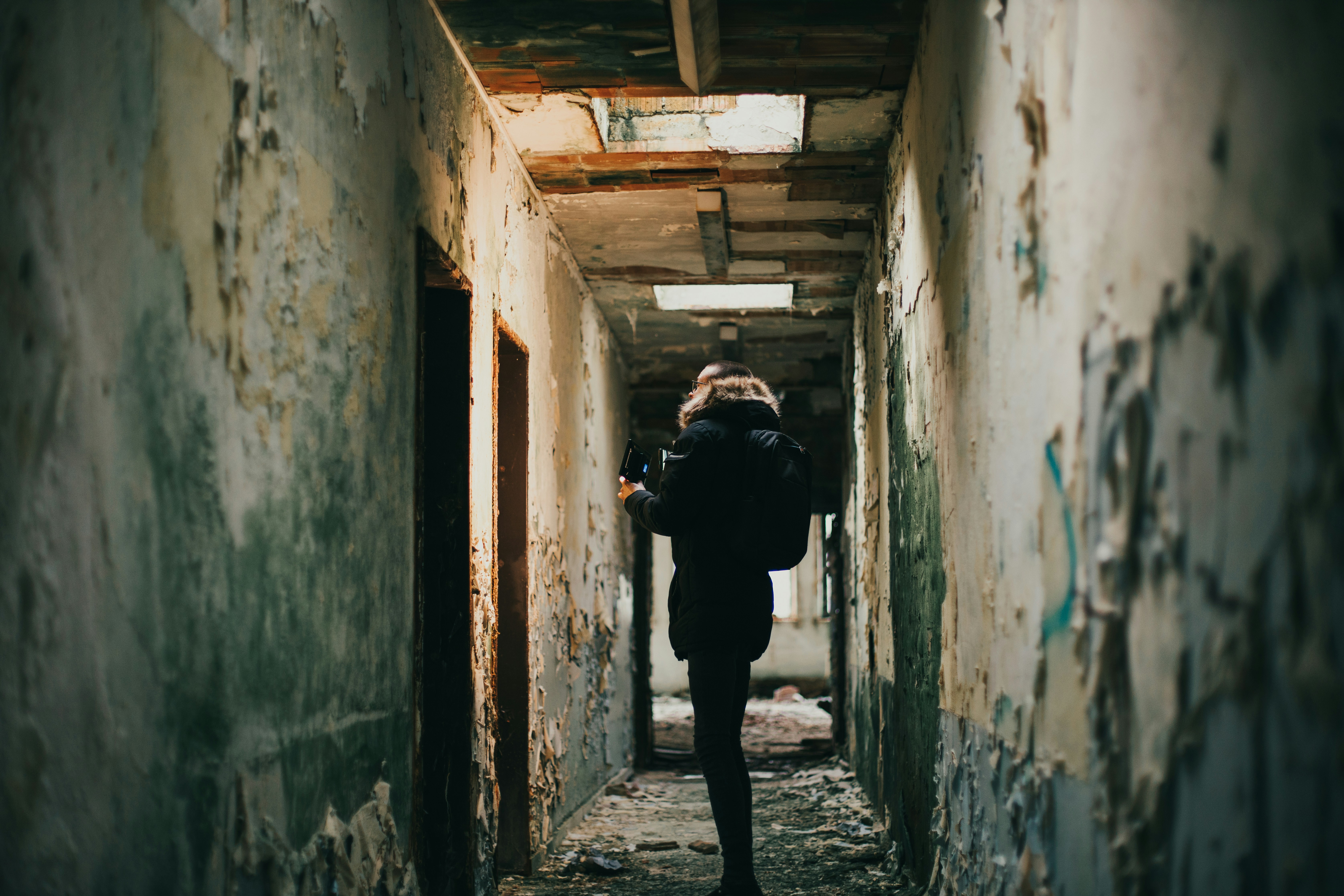 Person walking through a decaying hallway with exposed beams and peeling walls.