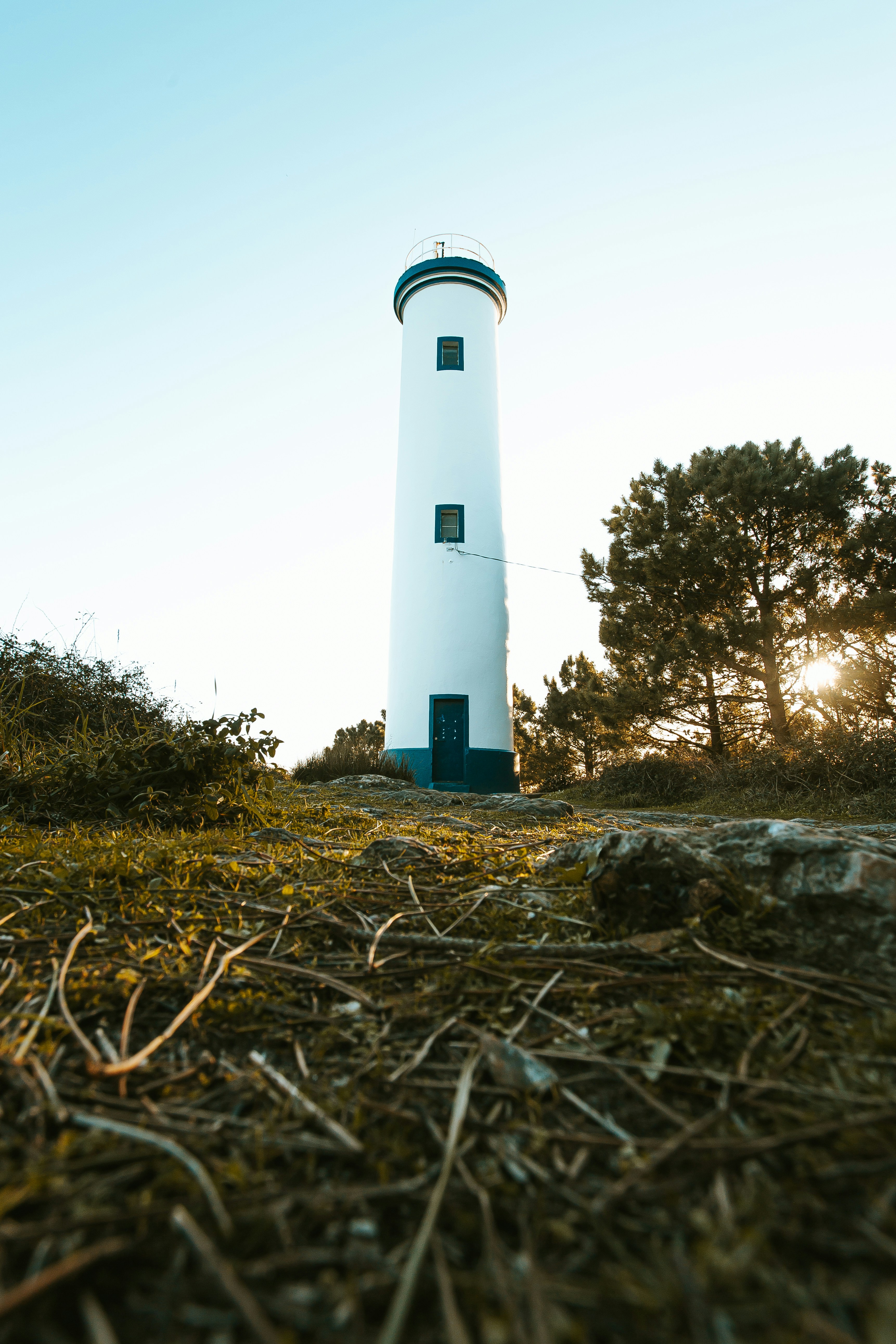 A lighthouse stands tall against a clear sky, surrounded by lush greenery and rocky terrain, capturing the essence of coastal navigation.
