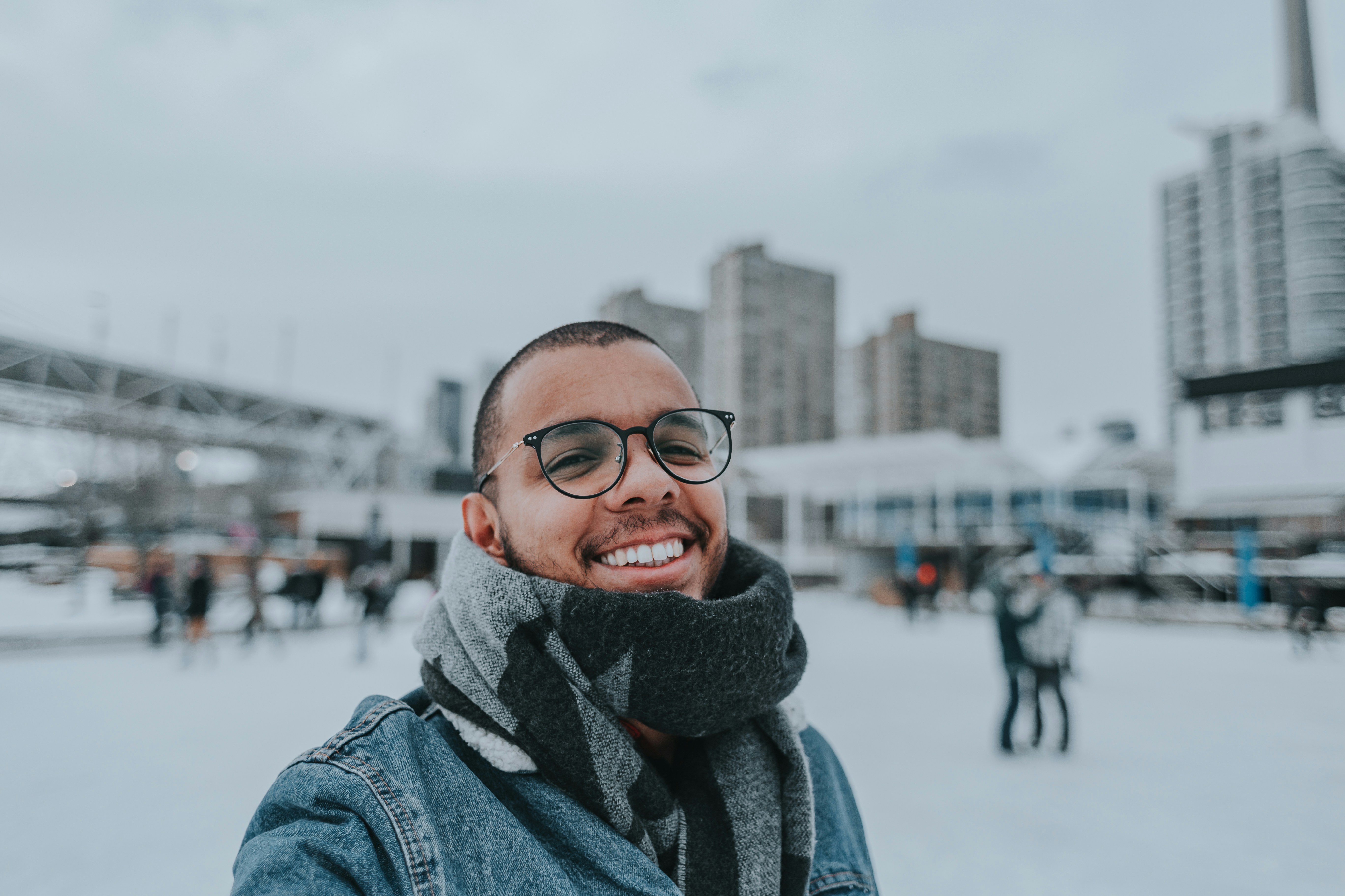 Person smiling warmly in a winter coat against an urban backdrop of Toronto's Harbourfront.