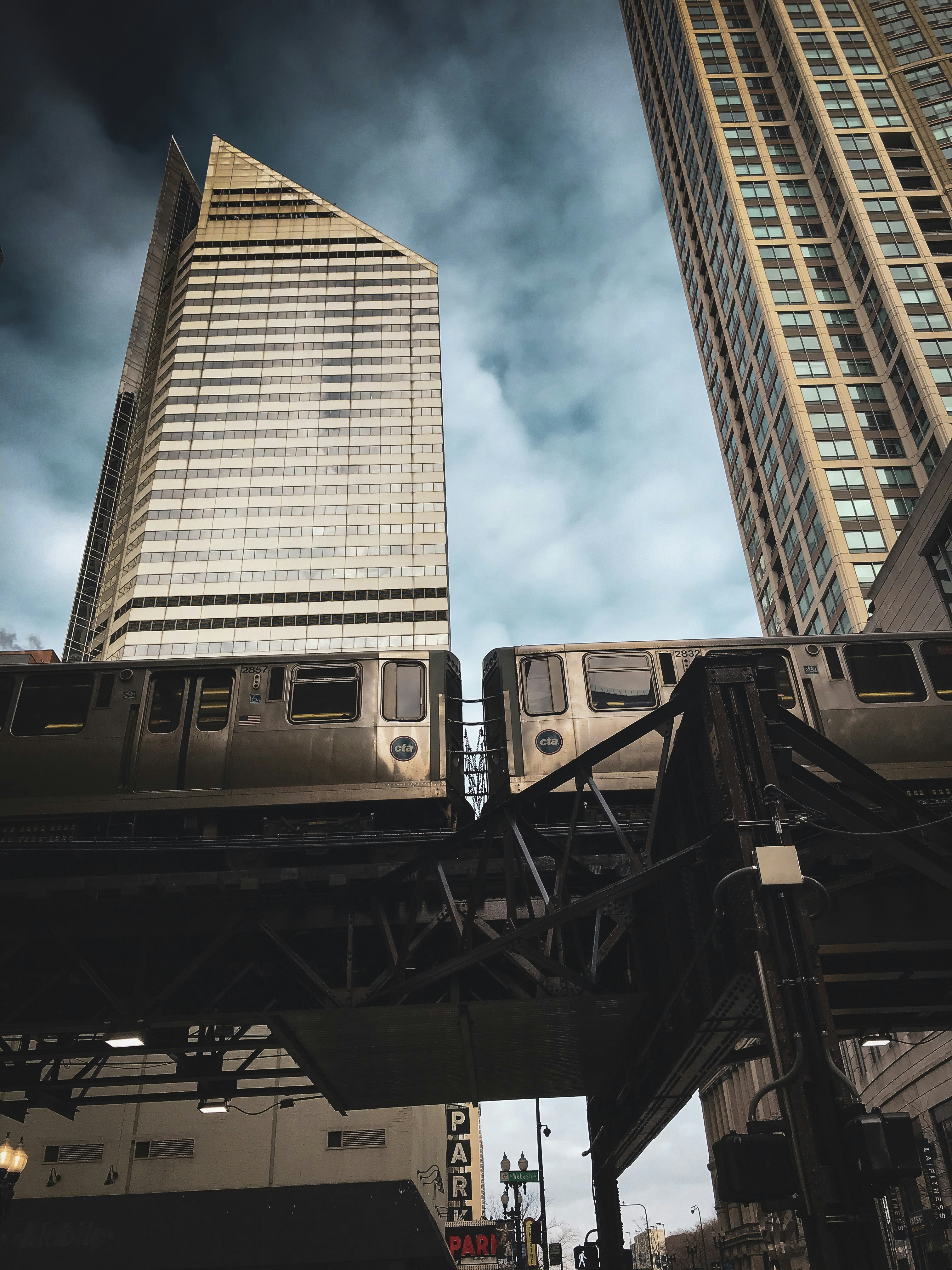 Elevated train gliding through a cityscape dominated by towering skyscrapers under a dramatic sky.