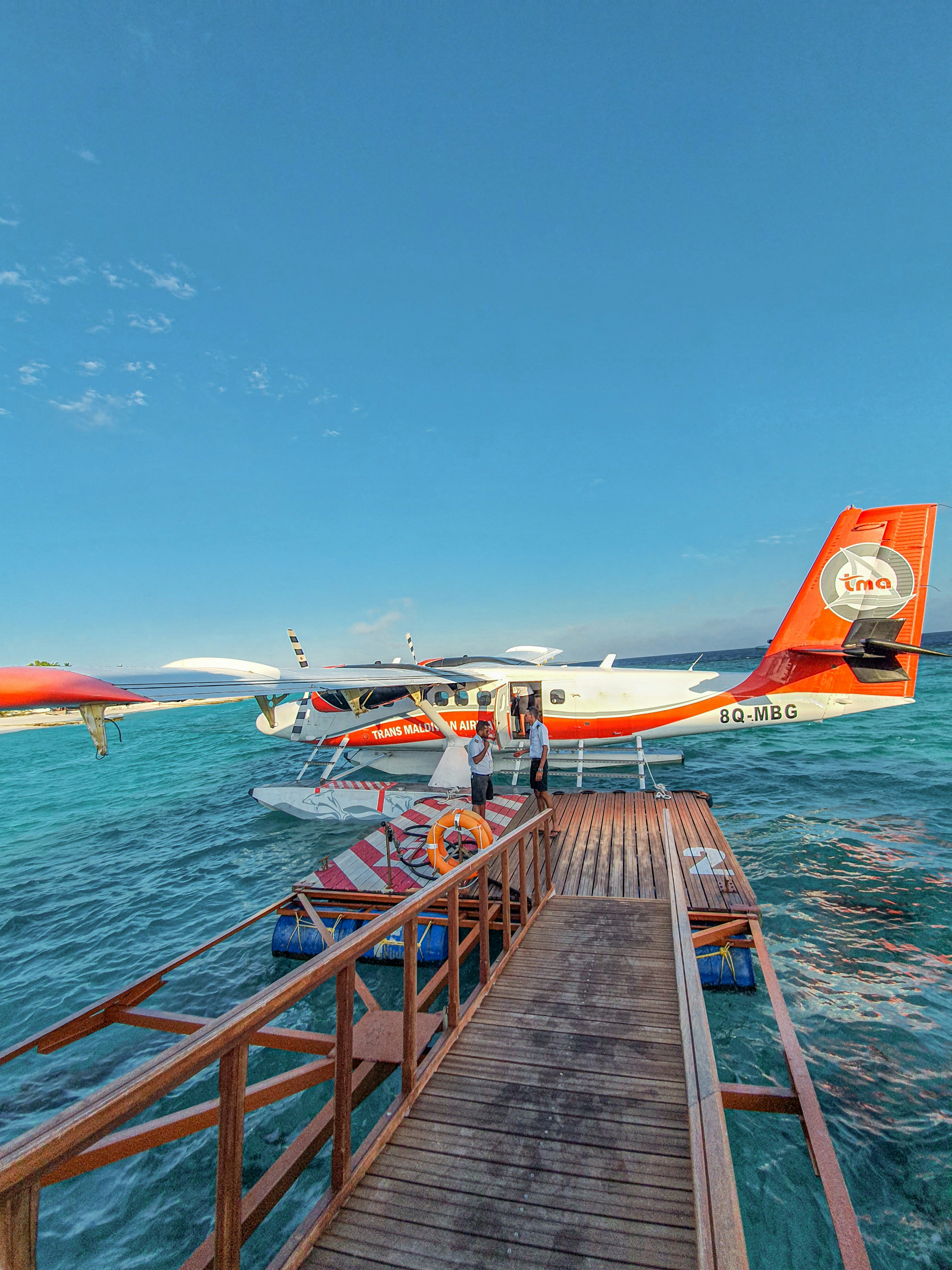 Seaplane docked at a wooden pier over turquoise waters, with crew members preparing for departure.