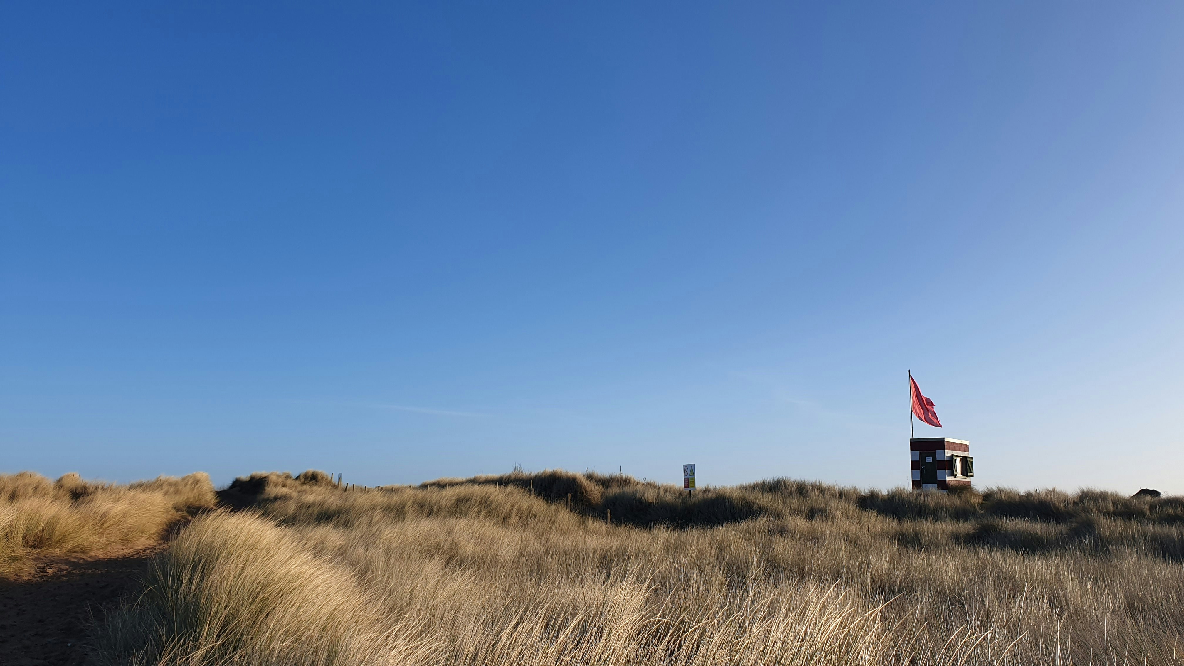 Flag on the Dune: A Quiet Coastal Outpost Under a Wide Blue Sky