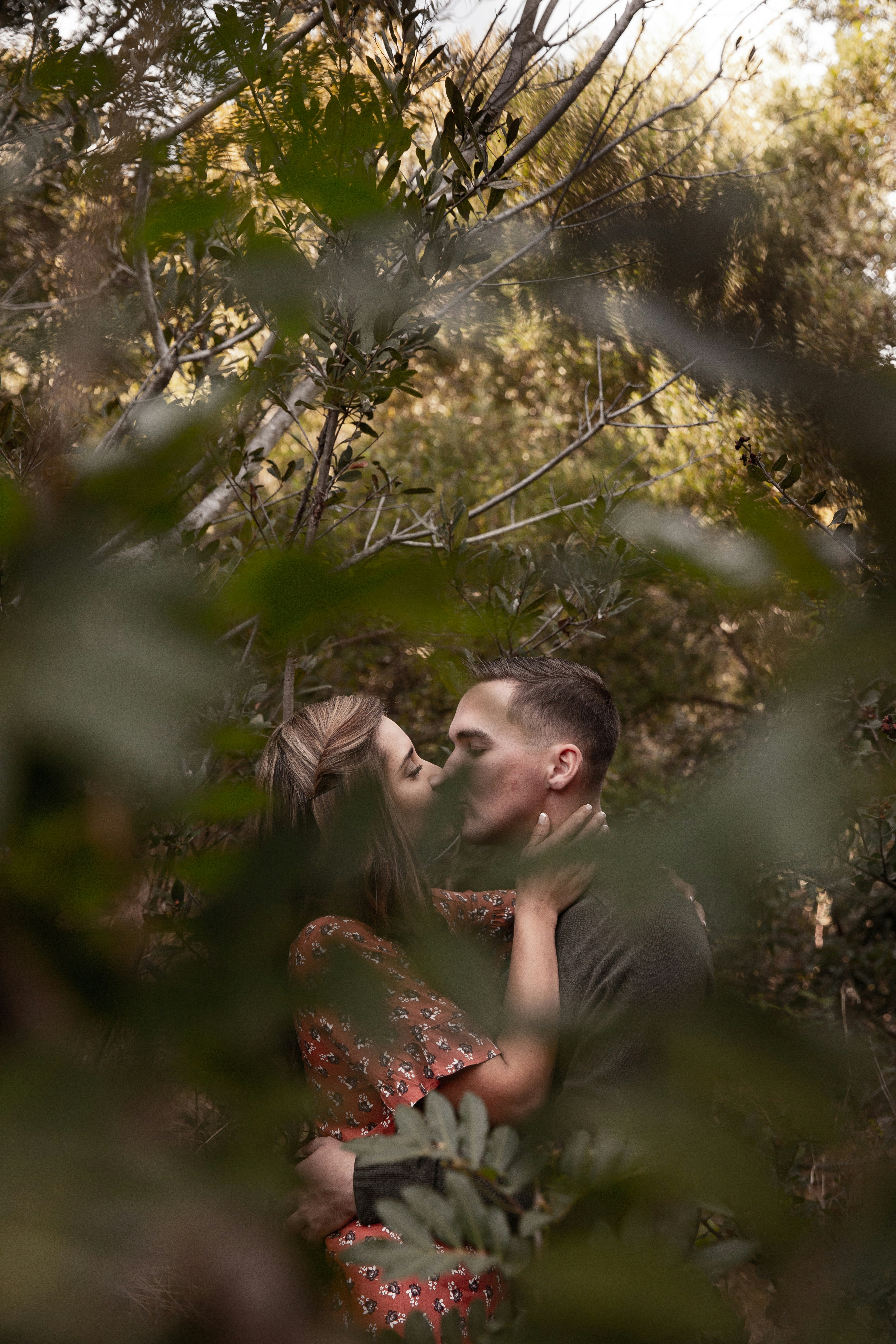 Couple sharing a tender kiss surrounded by lush greenery, capturing an intimate moment in nature.