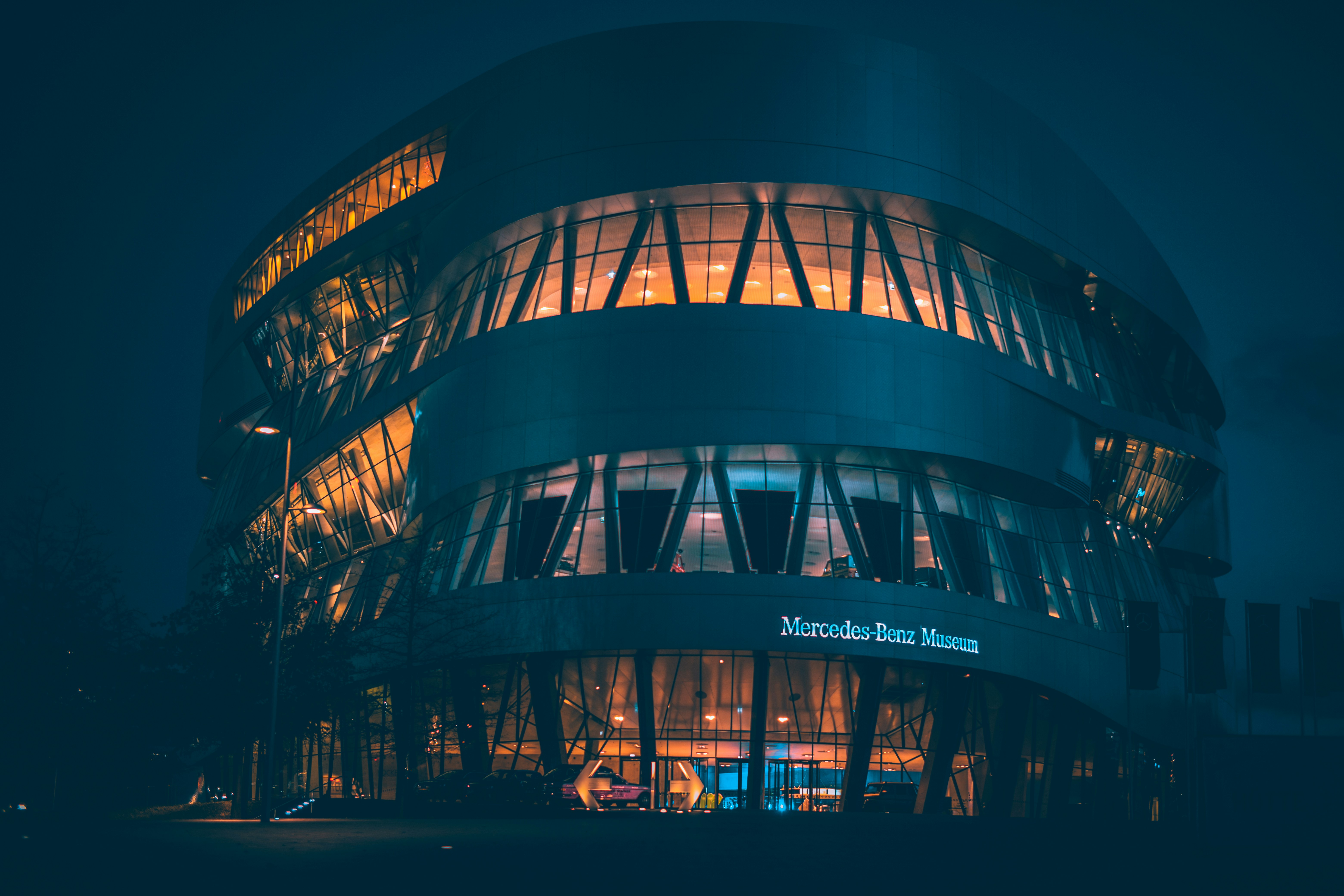 The Mercedes-Benz Museum showcases its modern architecture, illuminated by warm lights against a twilight backdrop. The unique design highlights the blend of innovation and automotive history.