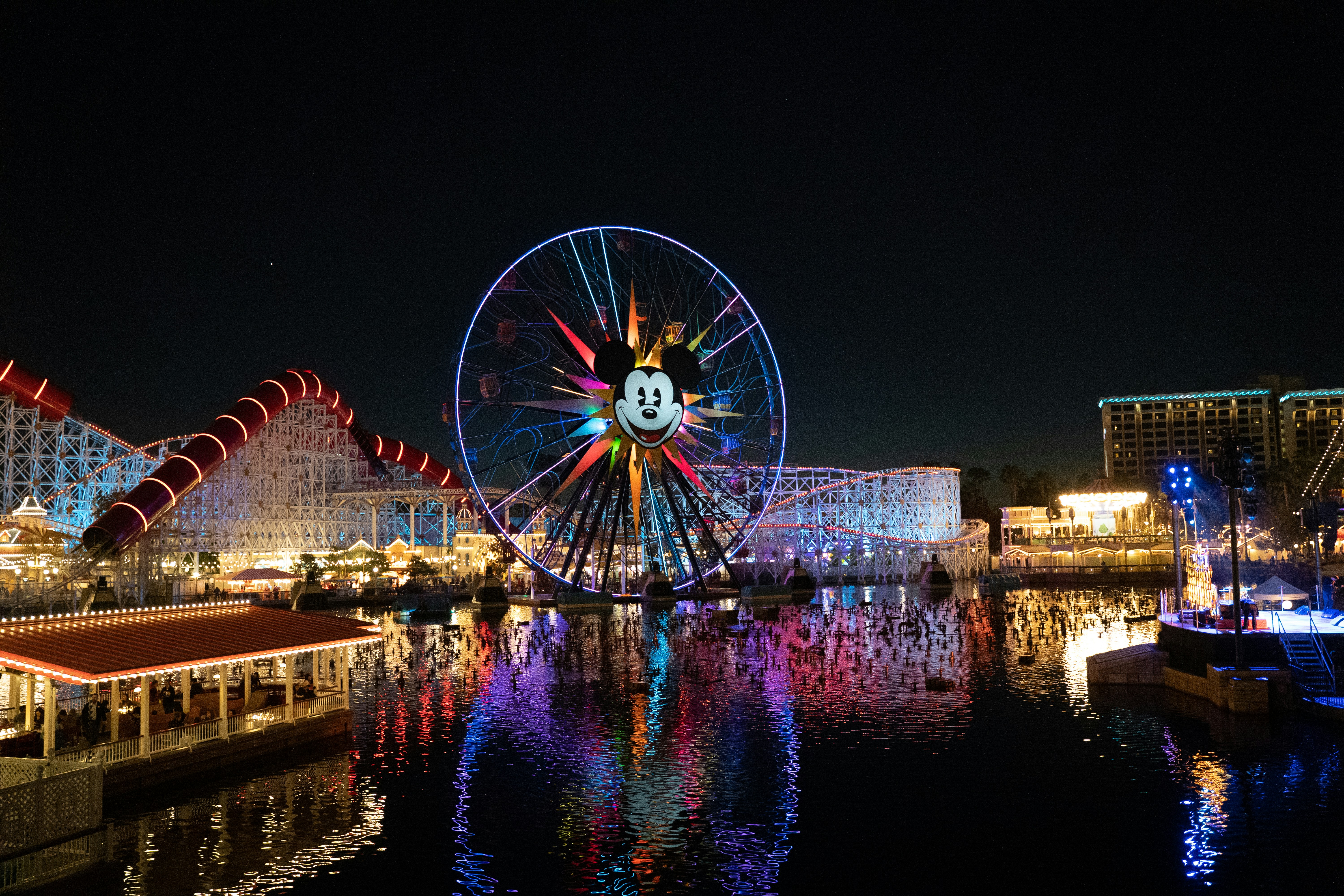 Illuminated Ferris wheel casting vibrant reflections on a calm waterfront at night.