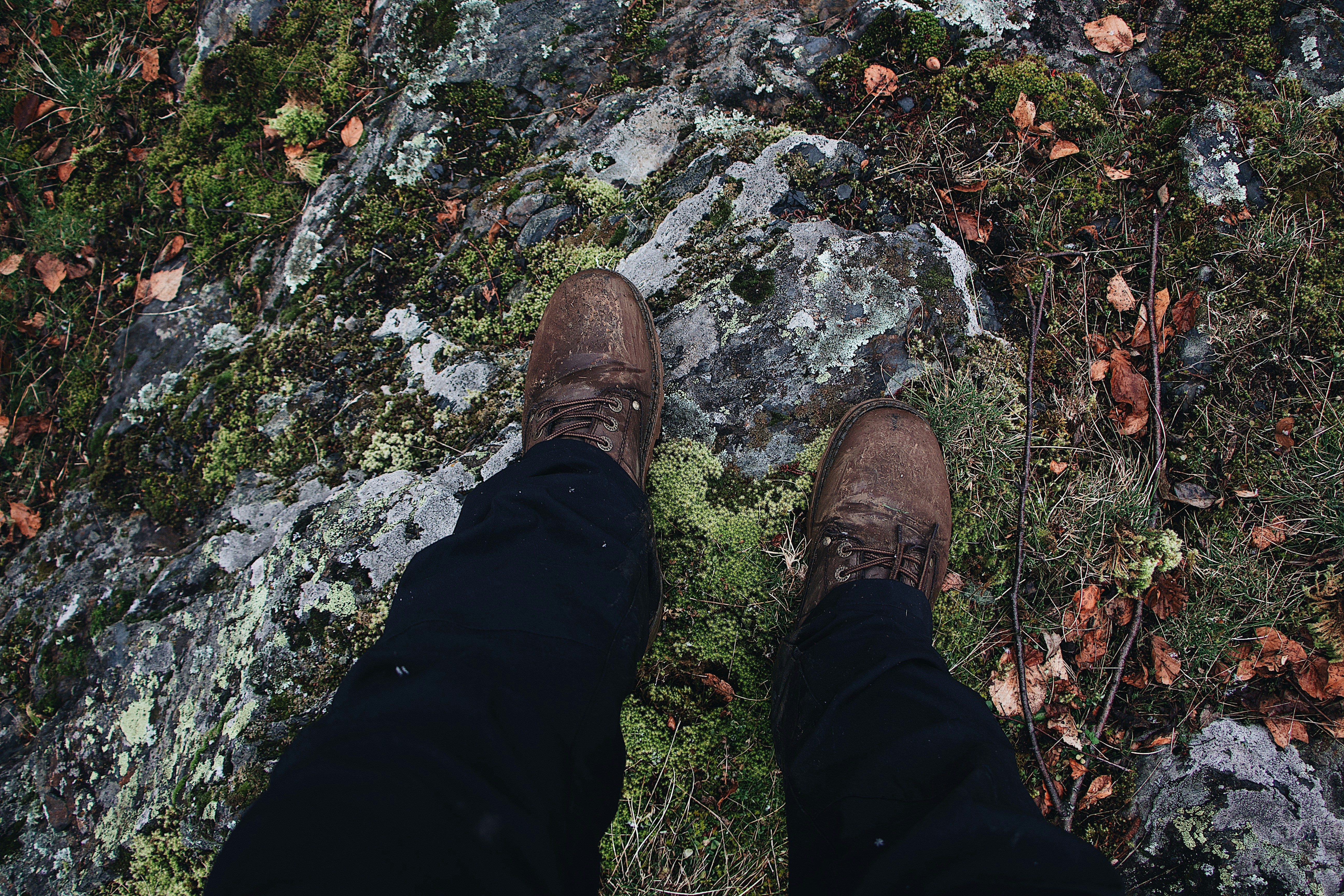 person in black pants and brown shoes standing on rocky ground