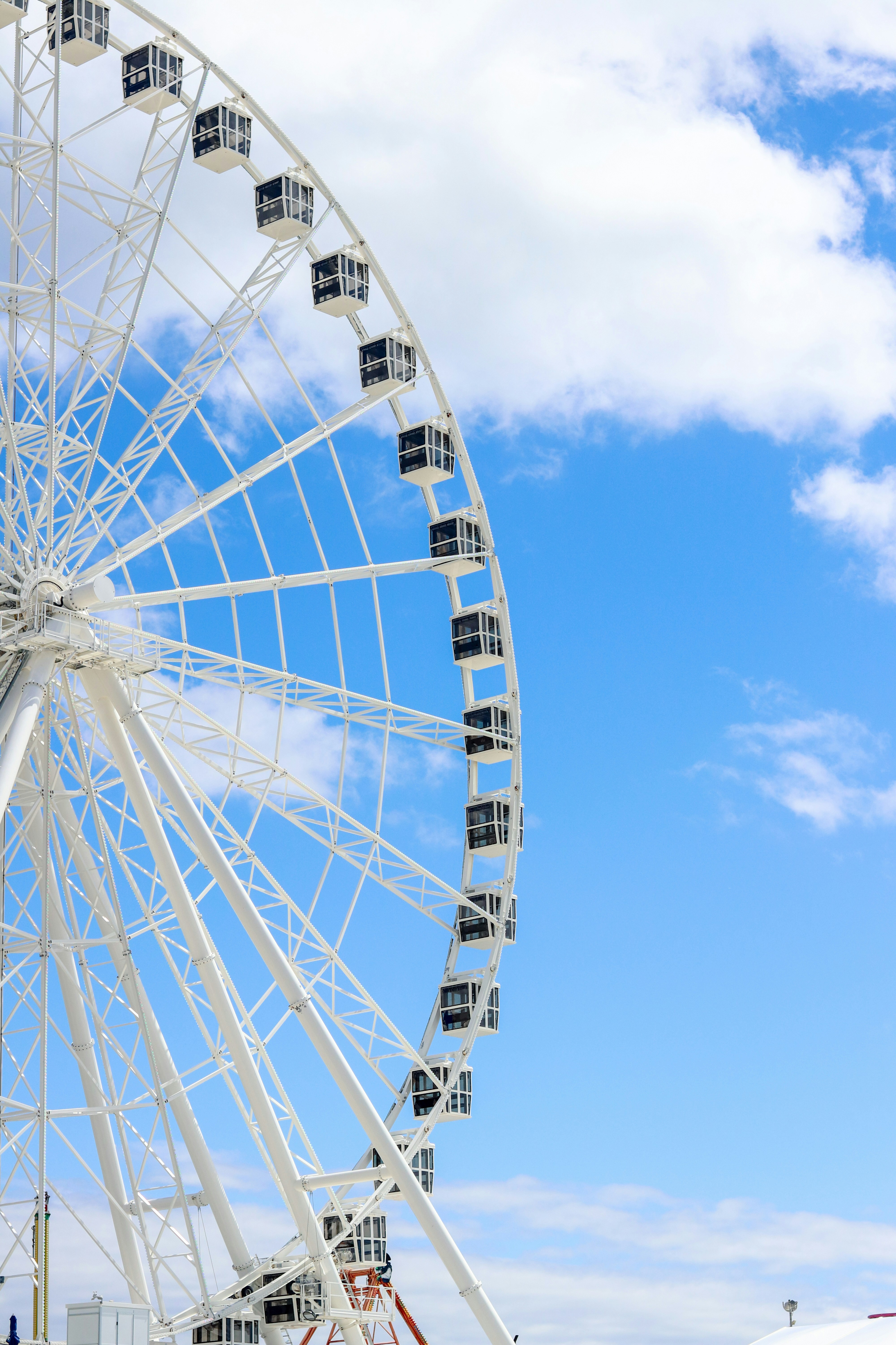 A large white Ferris wheel against a bright blue sky, showcasing its intricate structure and passenger cabins. The scene captures a moment of leisure and joy.