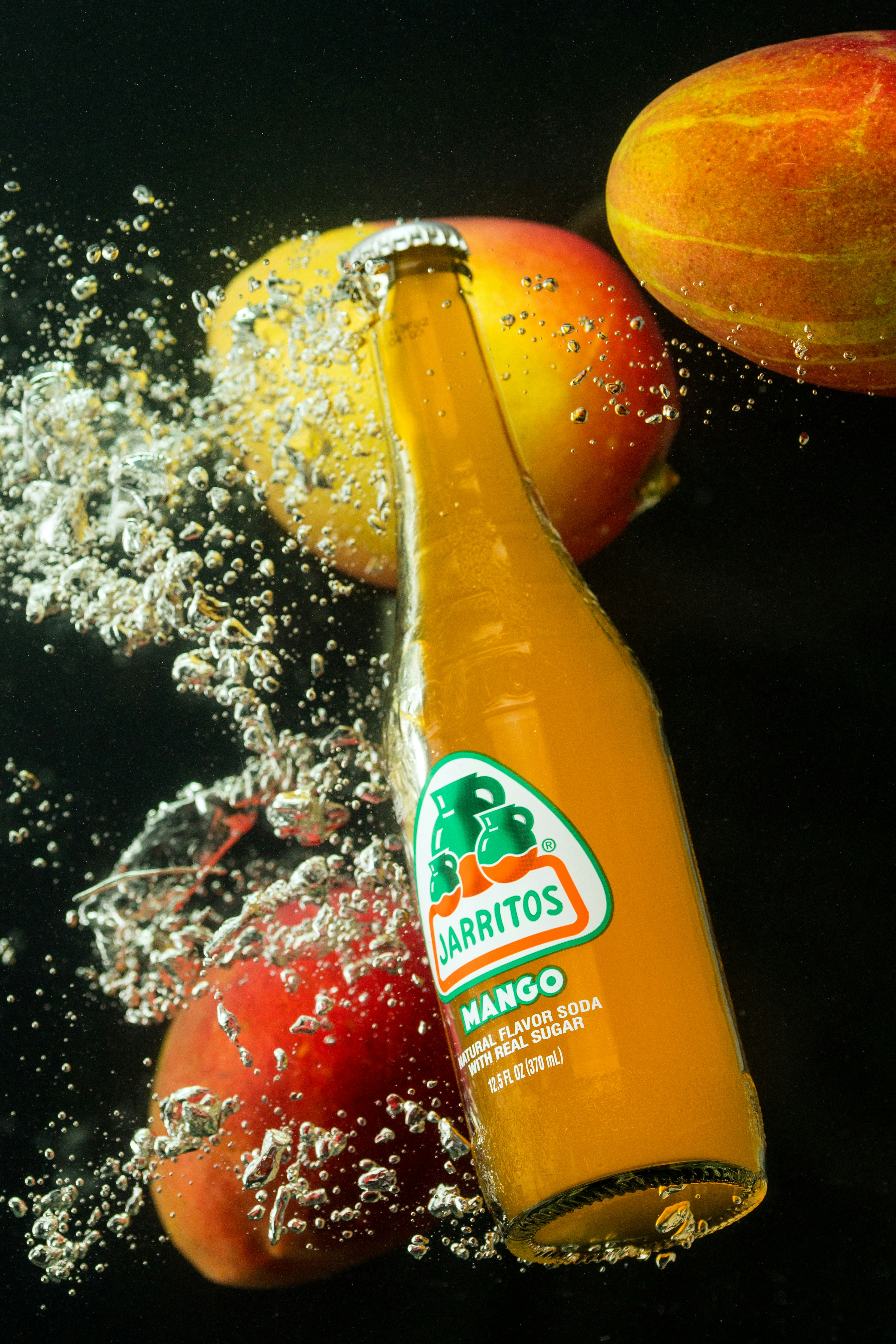 A Jarritos Mango soda bottle amidst a dynamic splash of bubbles, with ripe mangoes in the background. The scene captures the essence of refreshment.