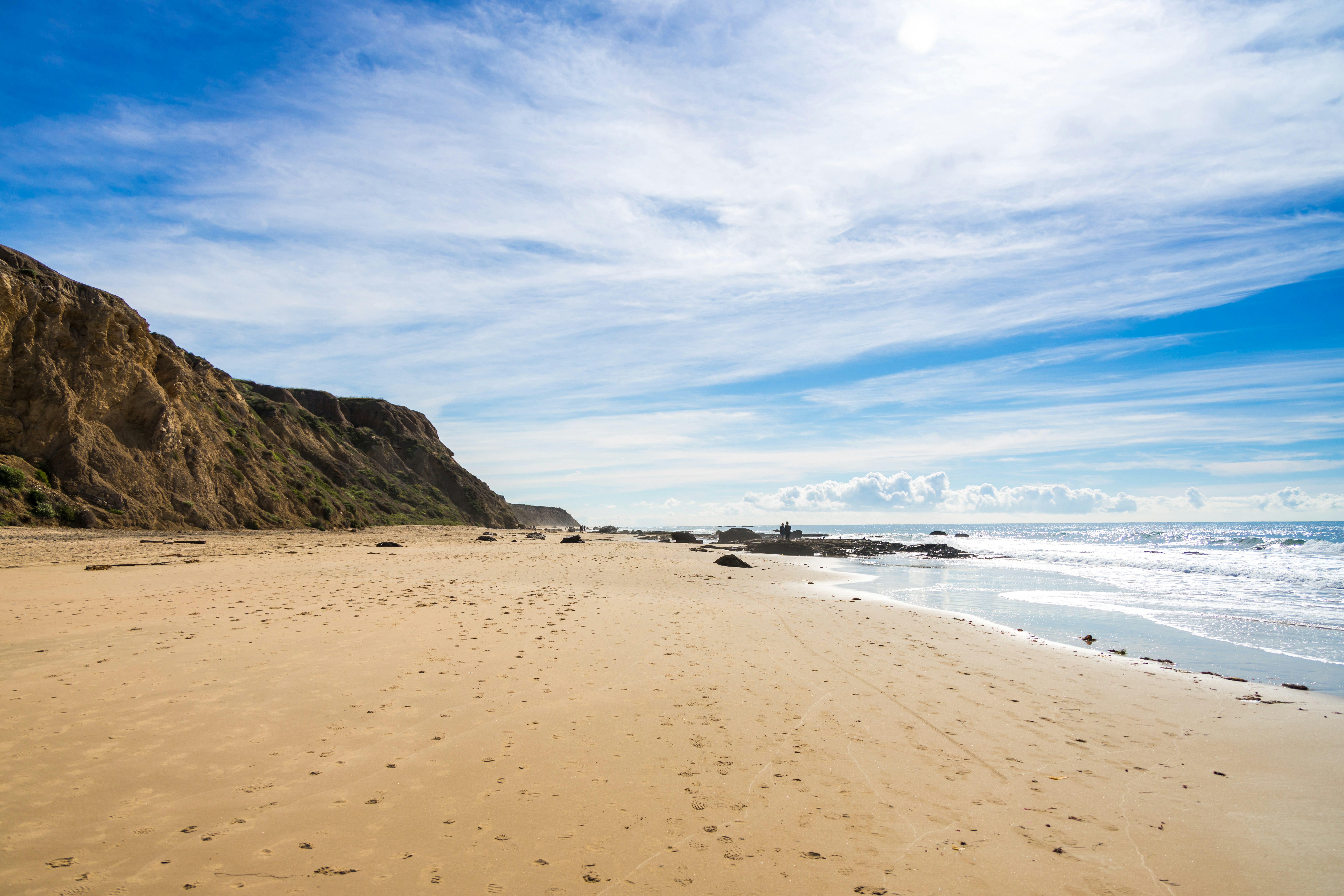 Expansive sandy beach with towering cliffs and a bright blue sky overhead.