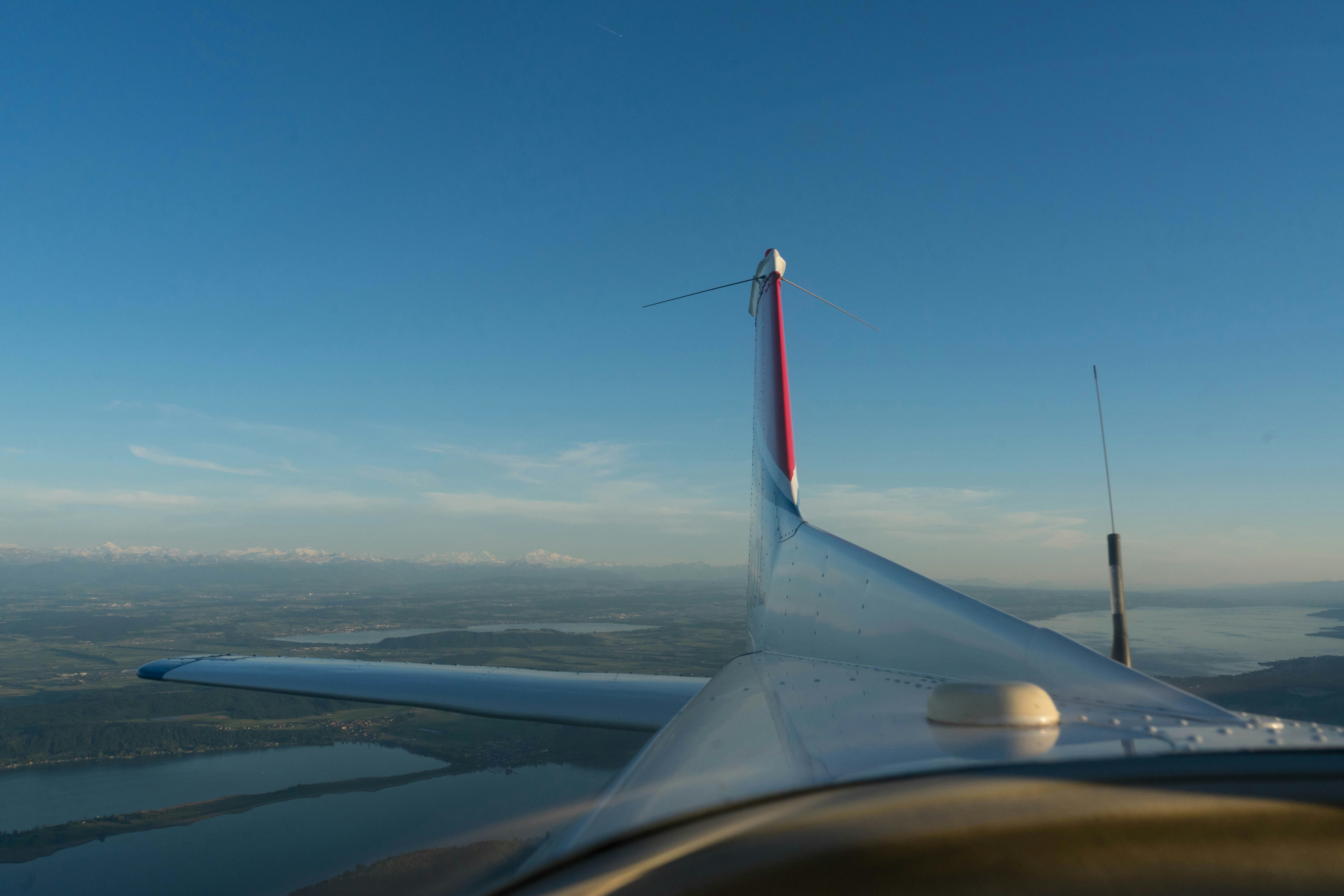 Airplane wing gliding above vast, serene waters under a clear blue sky.