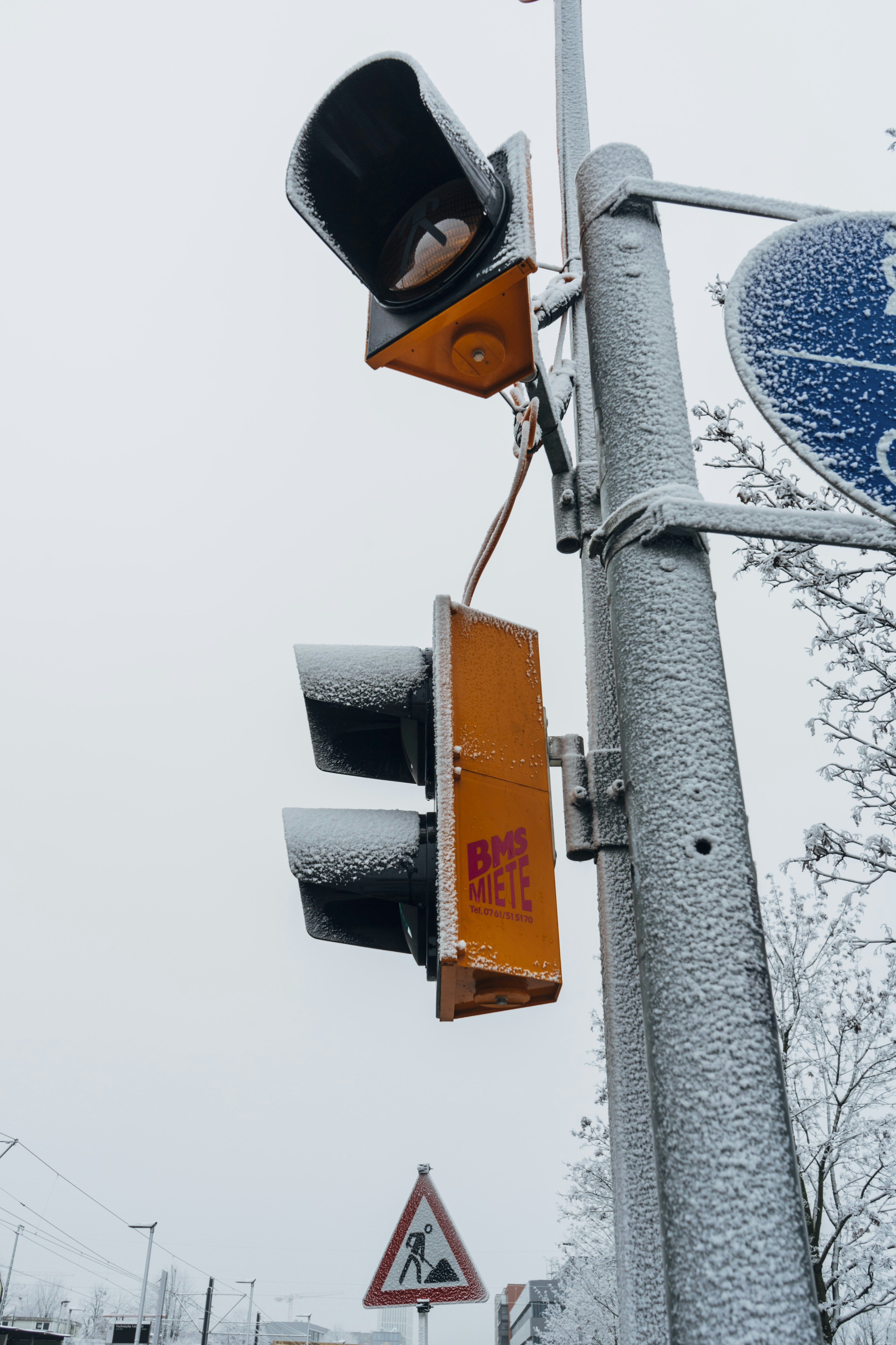 Frost-covered traffic signal and warning sign amidst a snowy landscape, emphasizing the chill of winter. The muted colors create a serene atmosphere.