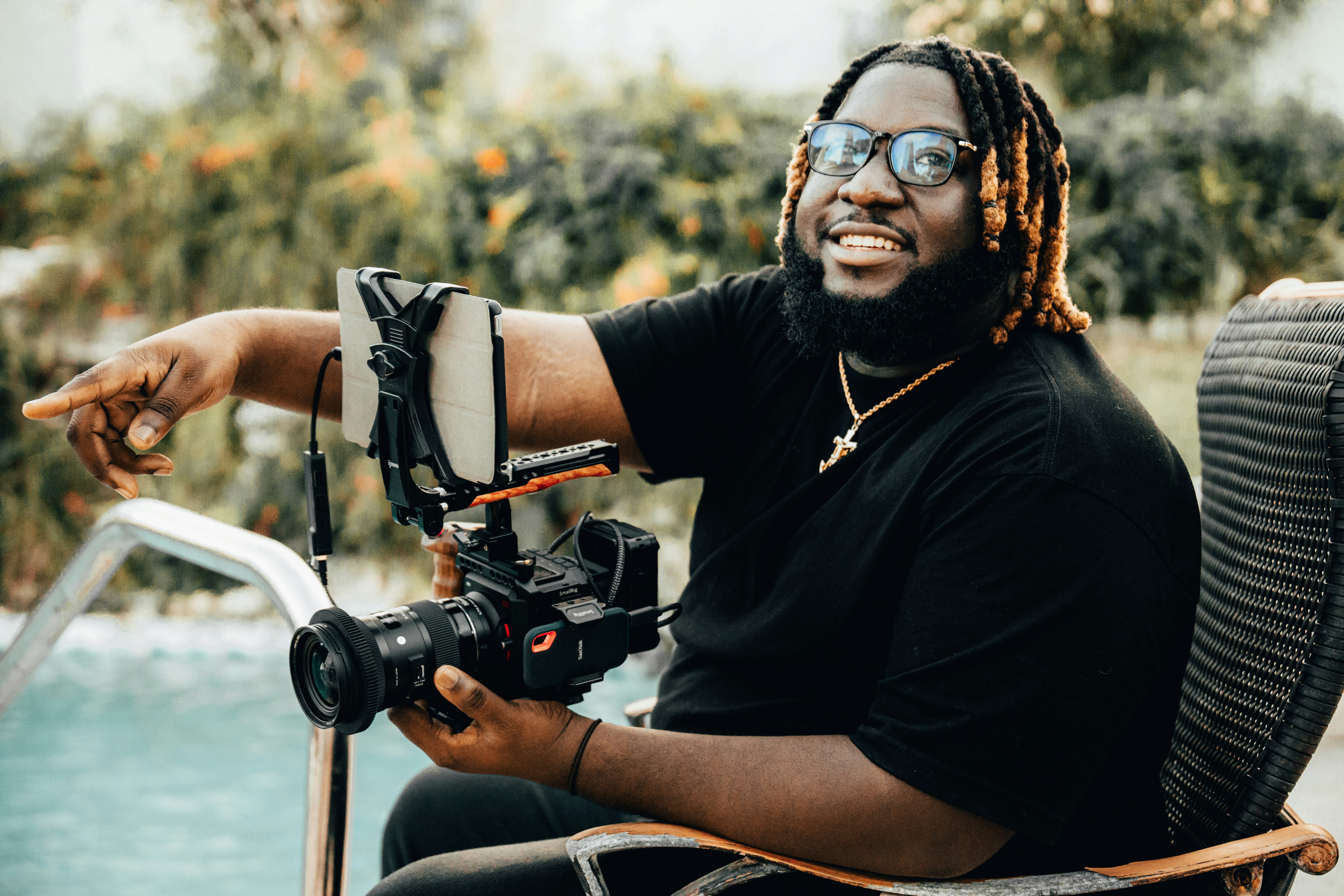Smiling person holding a Canon EOS R camera rigged with accessories by a pool.