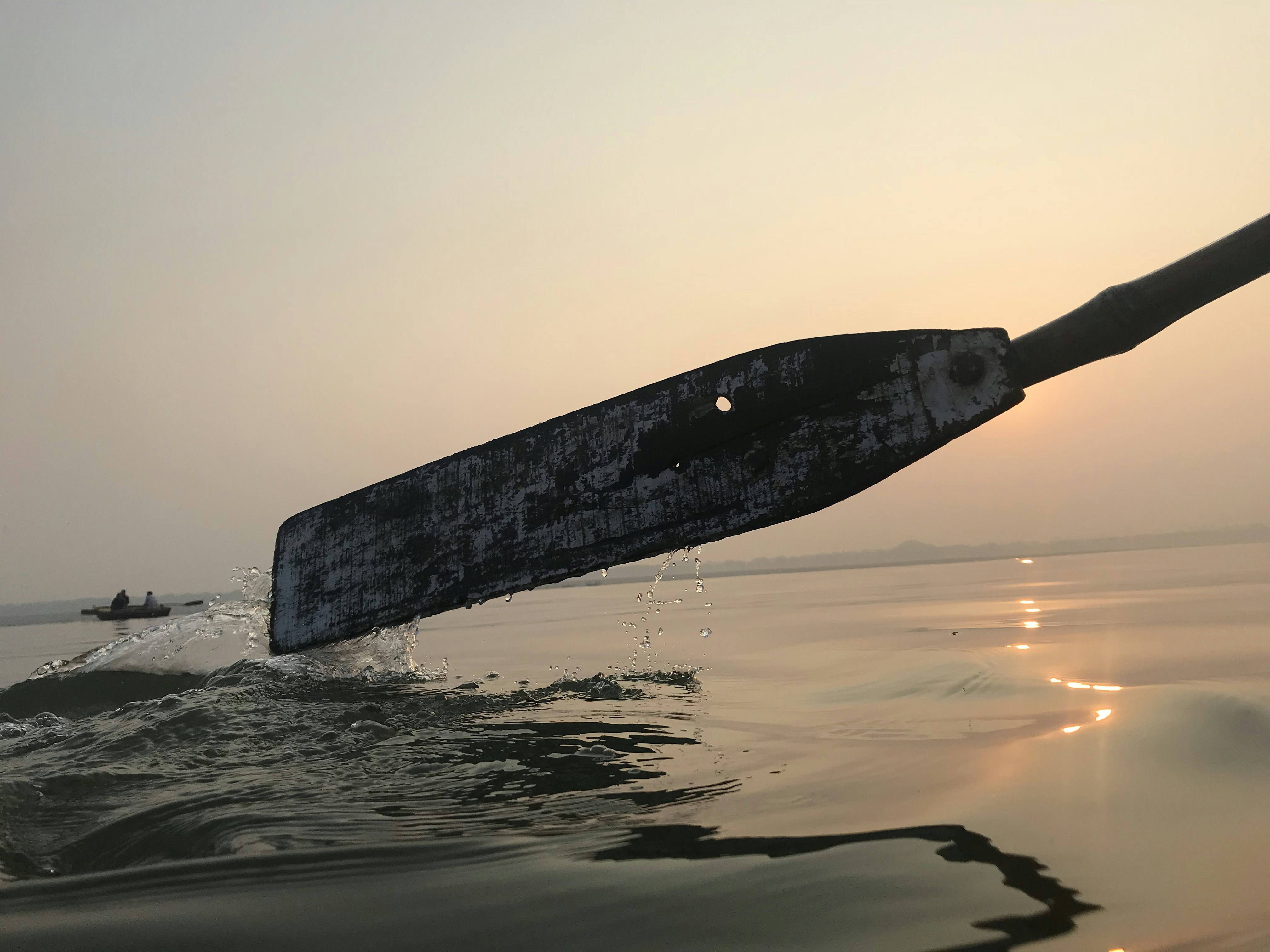 Weathered oar gliding through calm river waters at sunrise, casting gentle ripples.