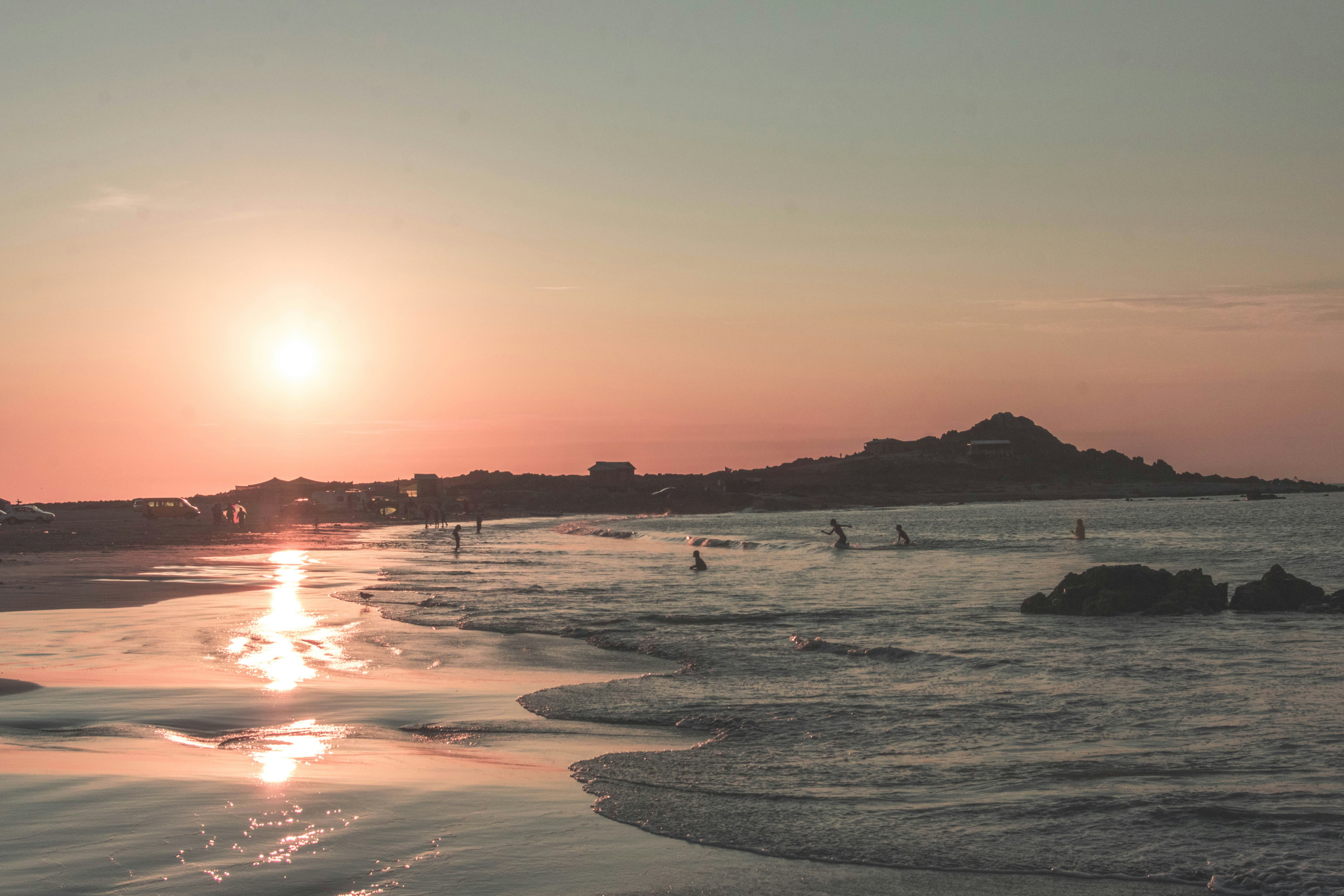 Silhouetted figures on a beach with the sun setting over the horizon casting a warm glow on the water.