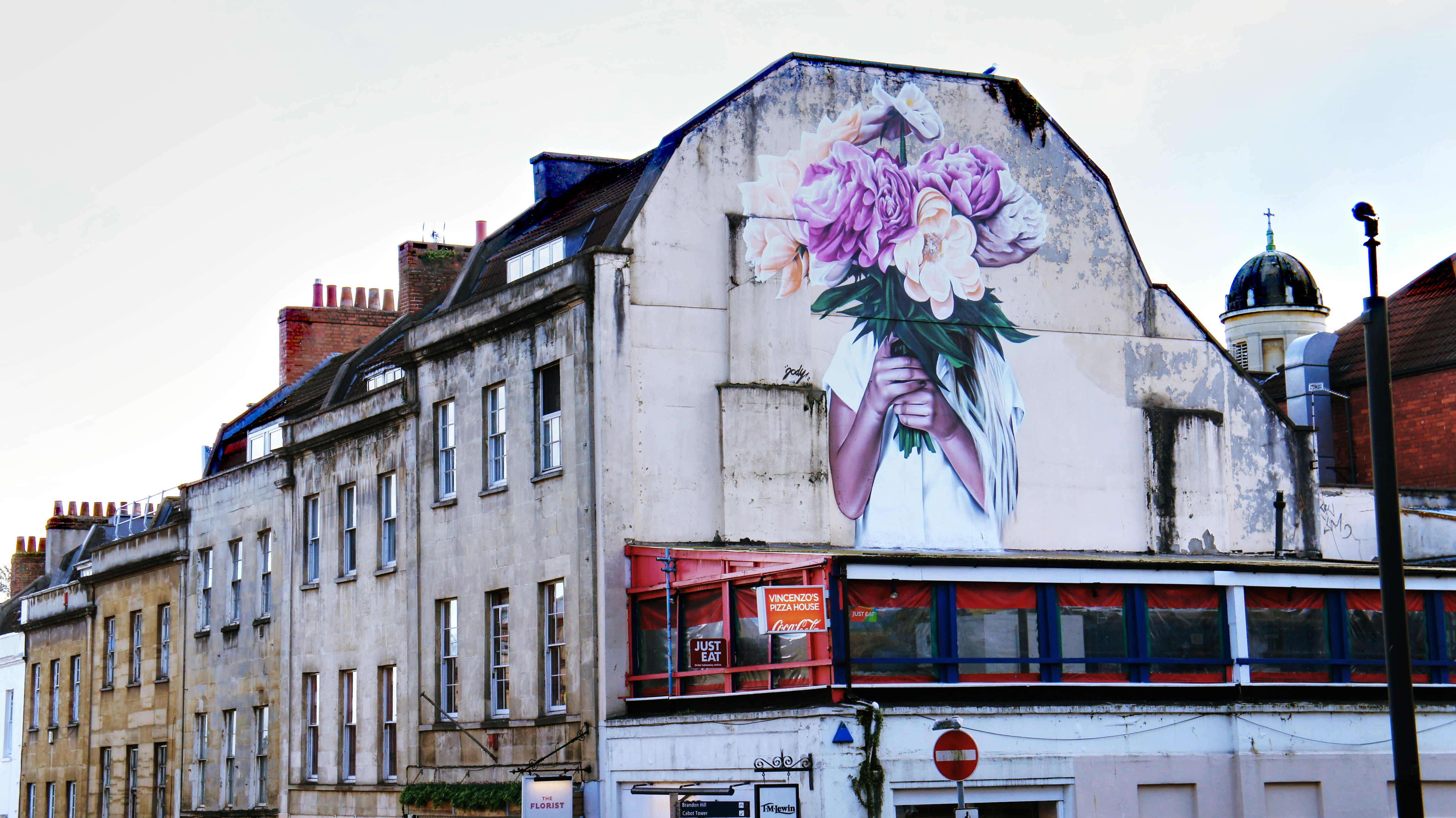Vibrant mural featuring a figure holding a bouquet of flowers on a weathered building facade.