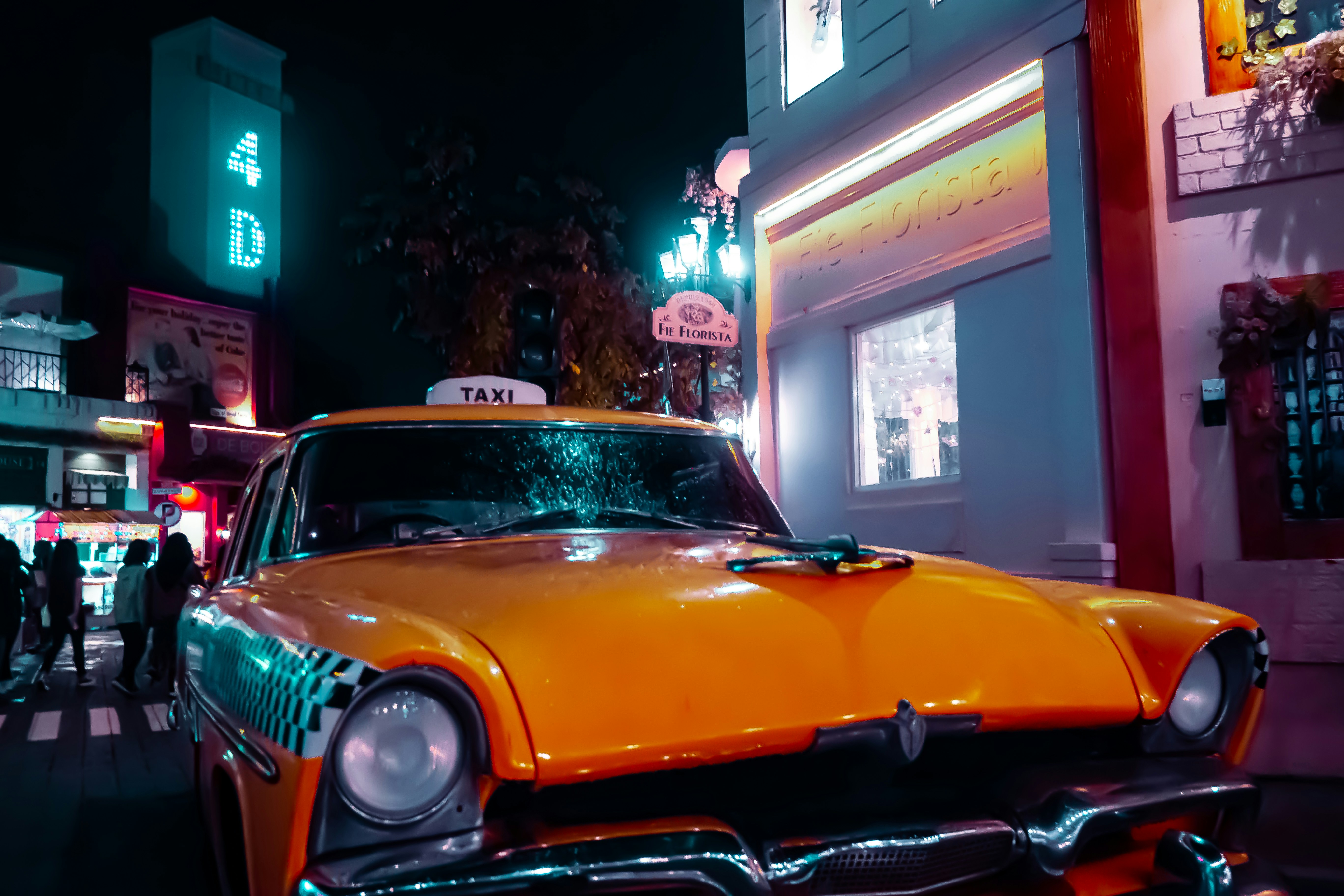Vintage yellow car parked under vibrant neon lights at night.